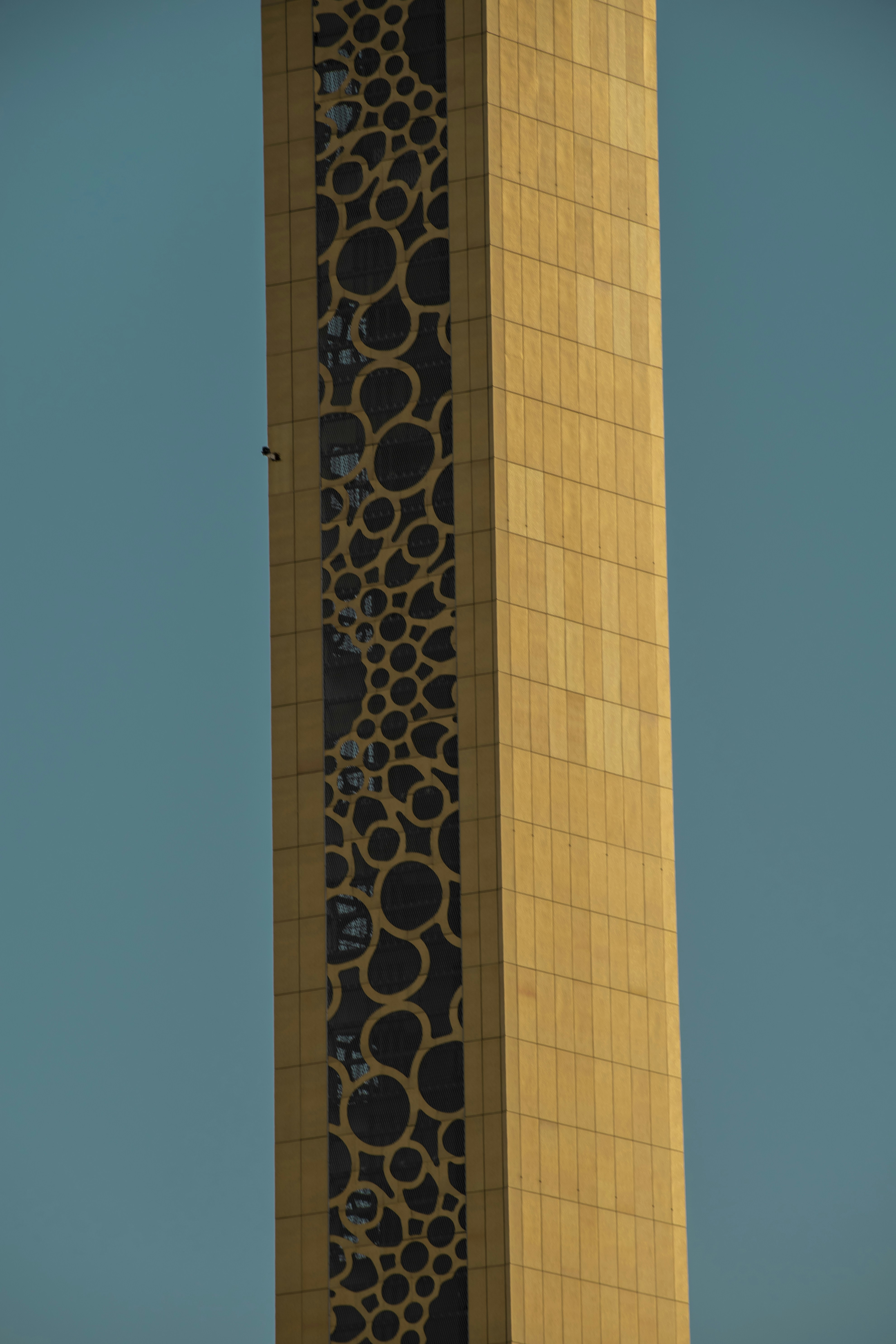 Tall architectural structure featuring a unique pattern of circular cutouts against a golden facade.