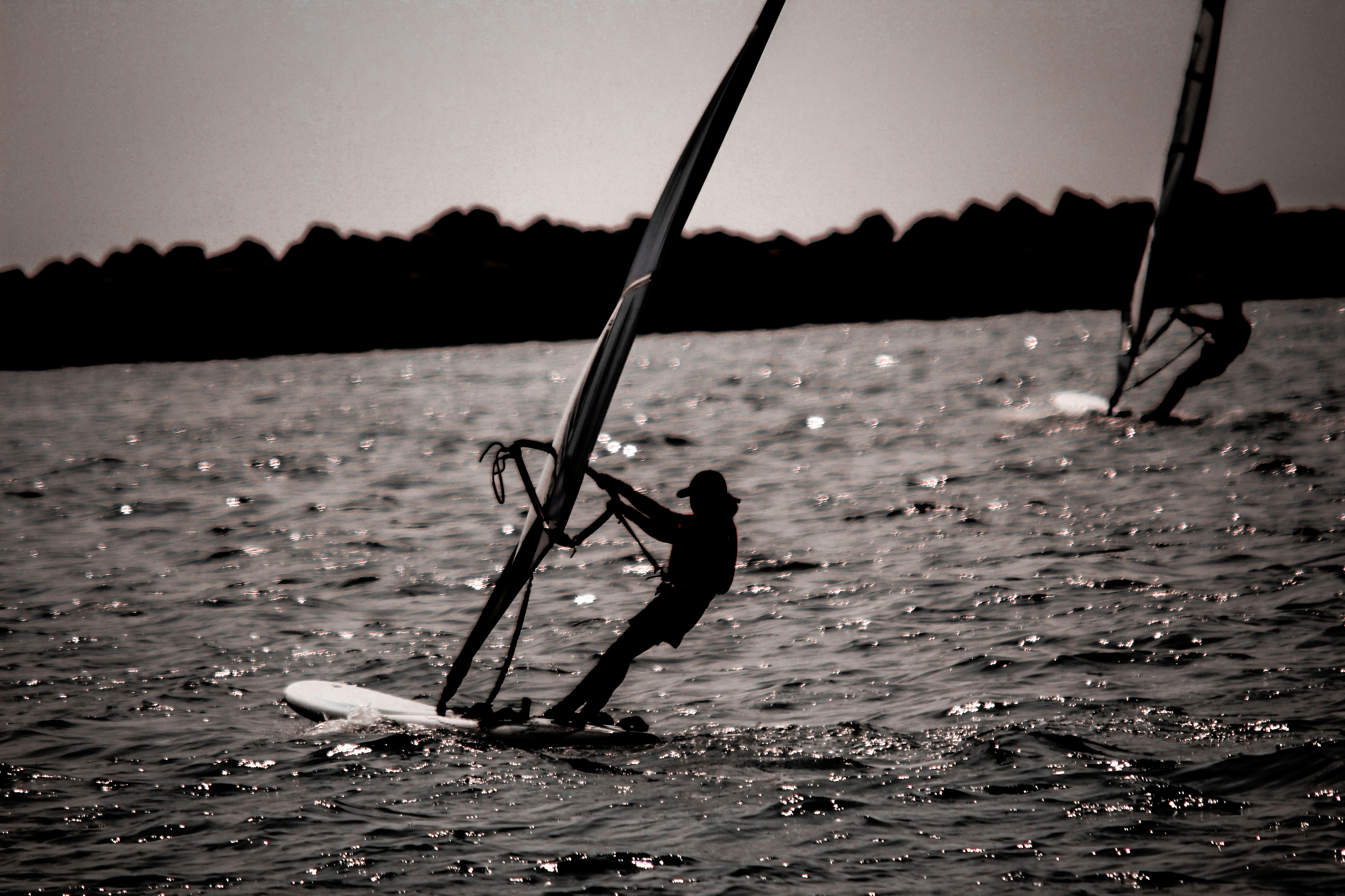 Silhouette on the Wake: Lone Windsurfer Carving Through Dusk