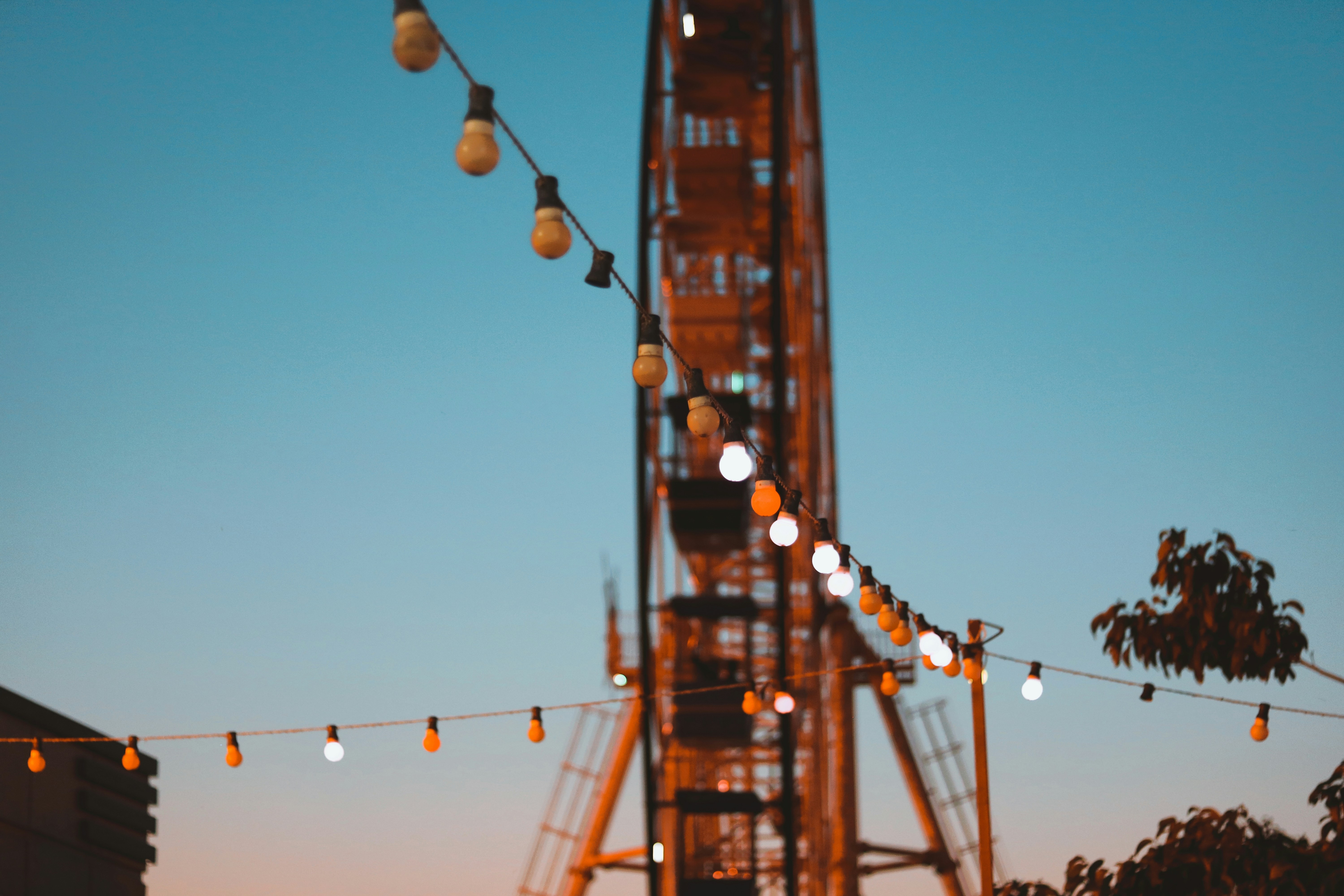 Colorful string lights illuminate a Ferris wheel against a twilight sky, creating a festive atmosphere.