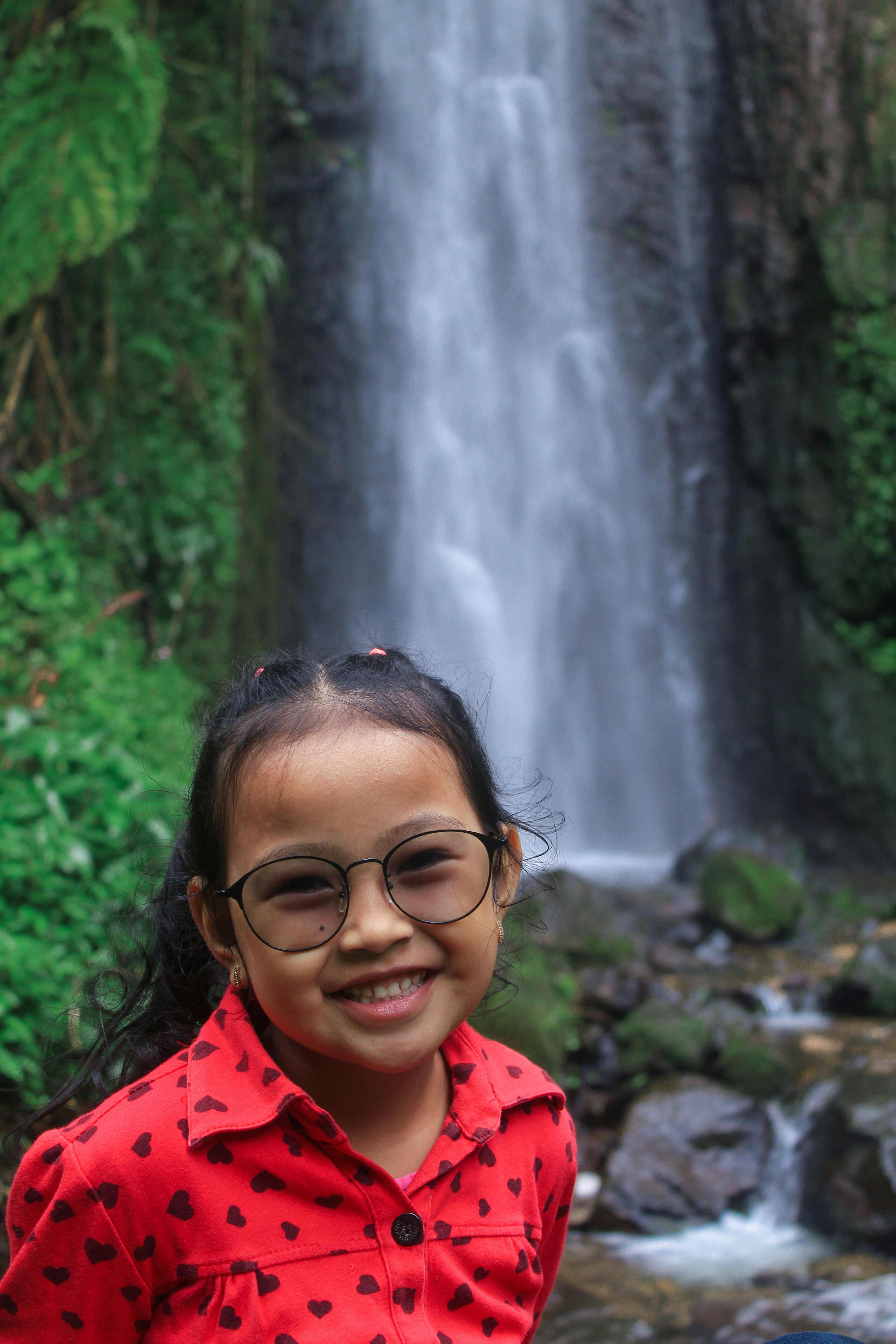 Girl in Red Shirt with Glasses Beside a Waterfall