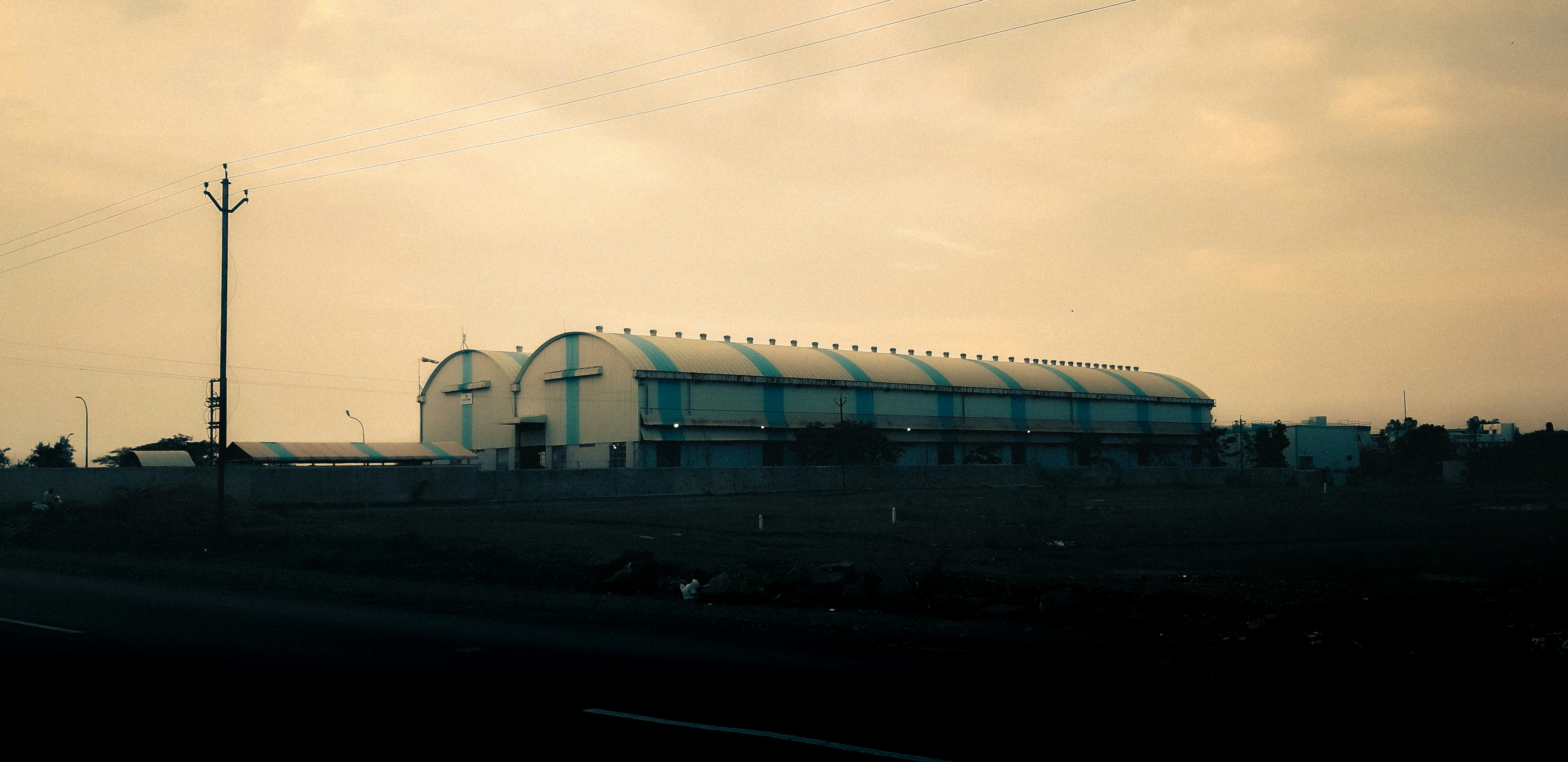 Large industrial building with an expansive roof under a cloudy sky.