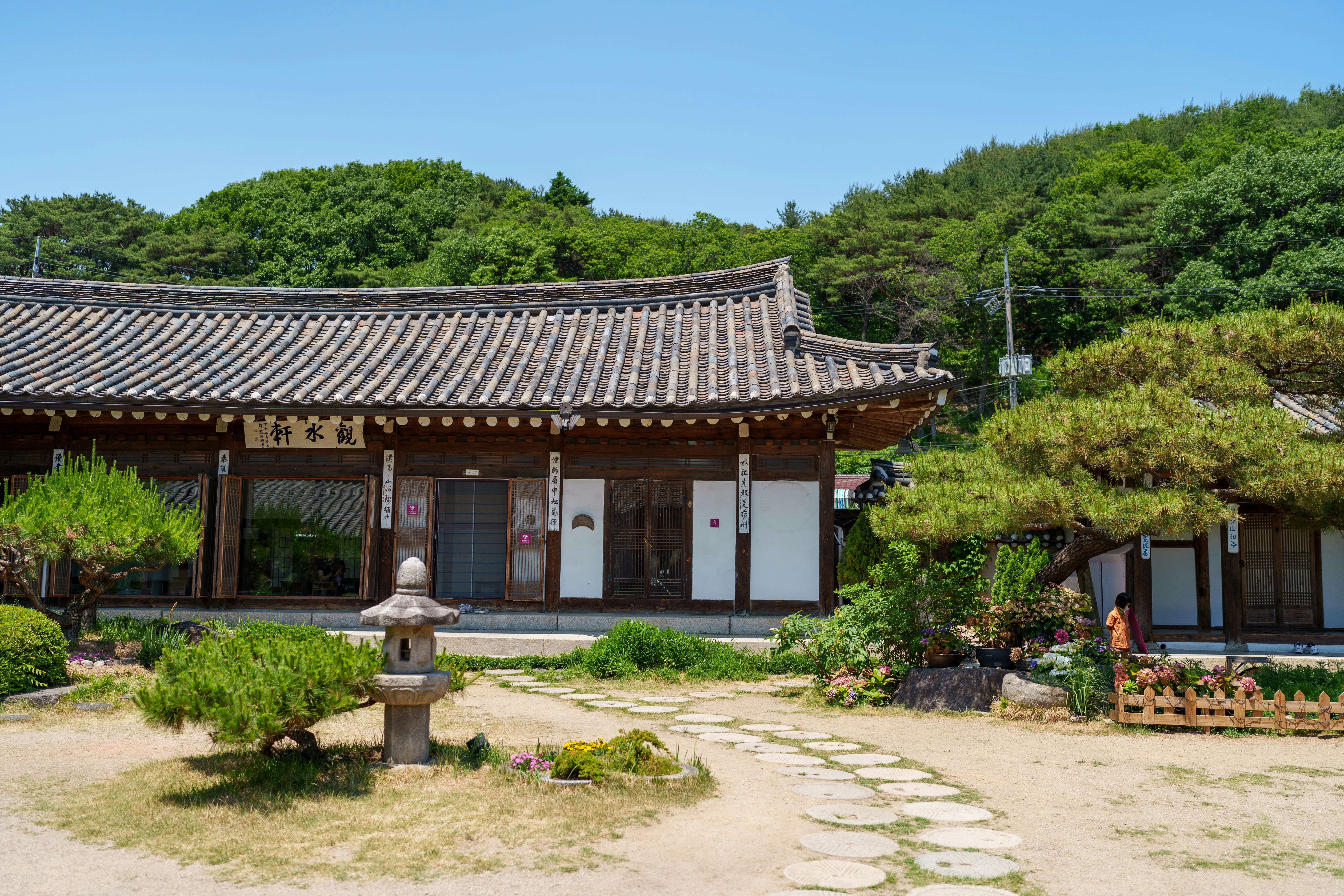 Traditional Korean house surrounded by lush greenery and a stone path leading through a serene garden.