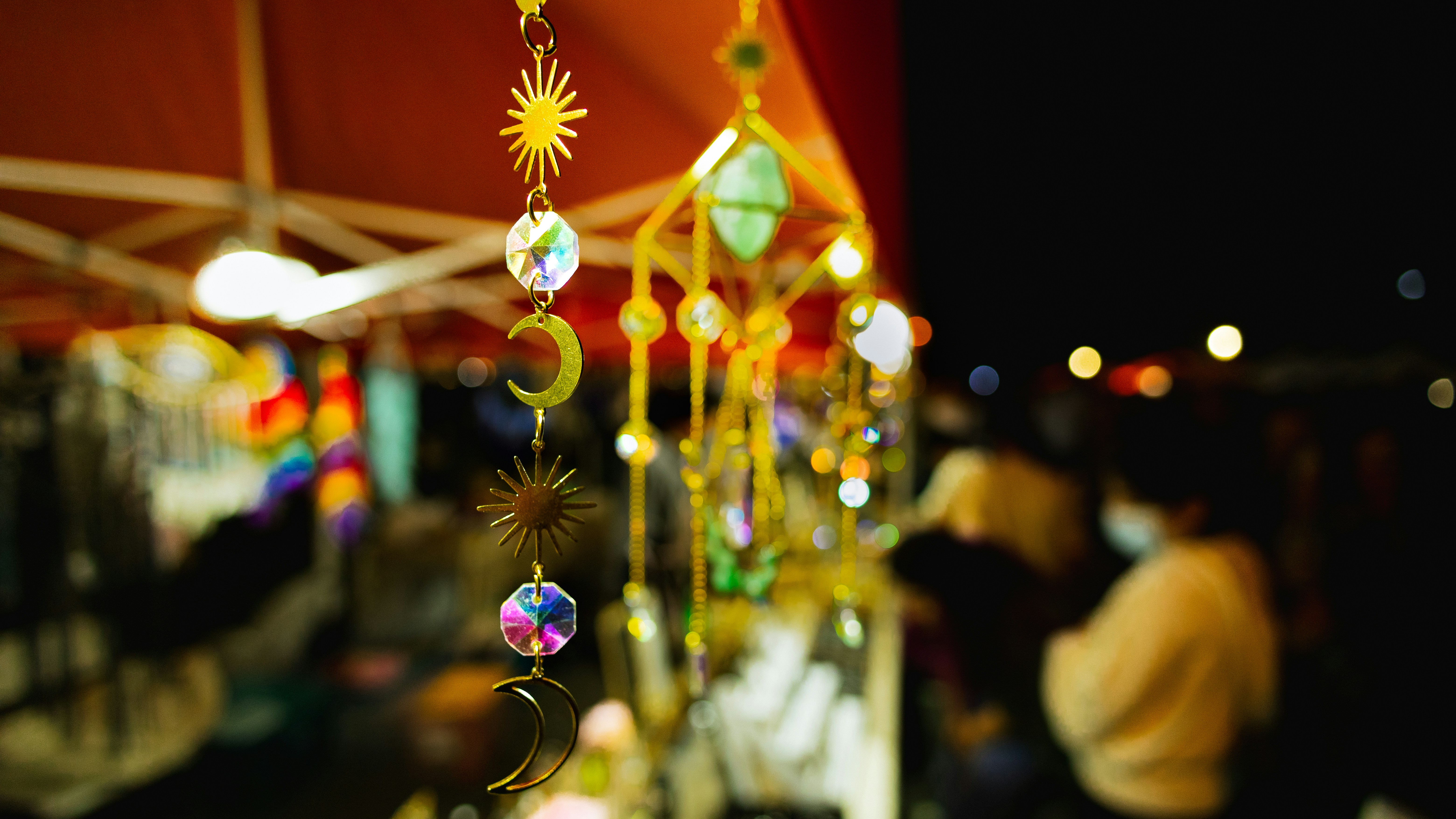 Colorful hanging ornaments illuminated under the warm glow of market stalls, creating a magical atmosphere at night.