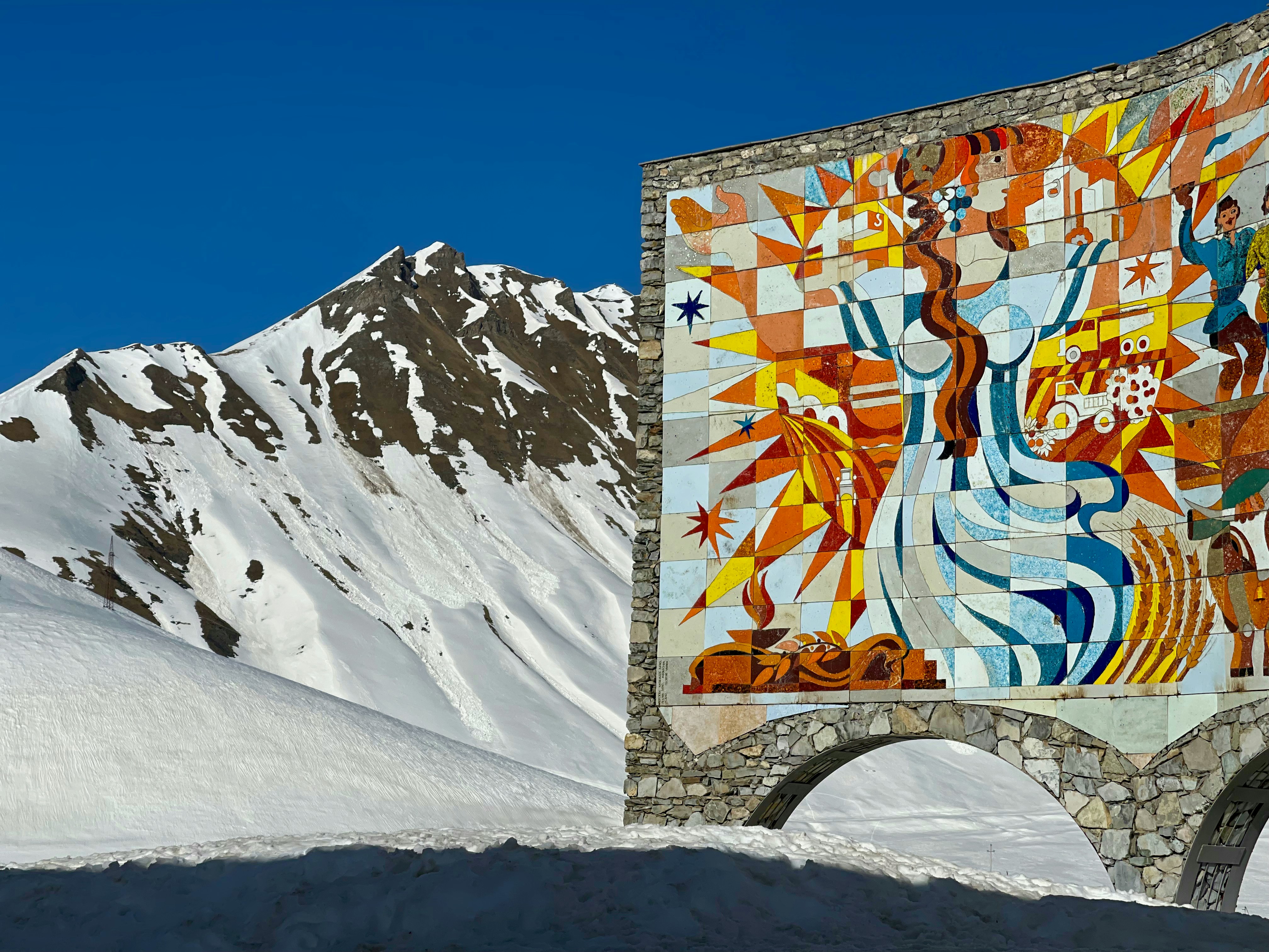 Colorful mural depicting a stylized figure amidst snowy peaks, showcasing vibrant artistry against a clear blue sky.