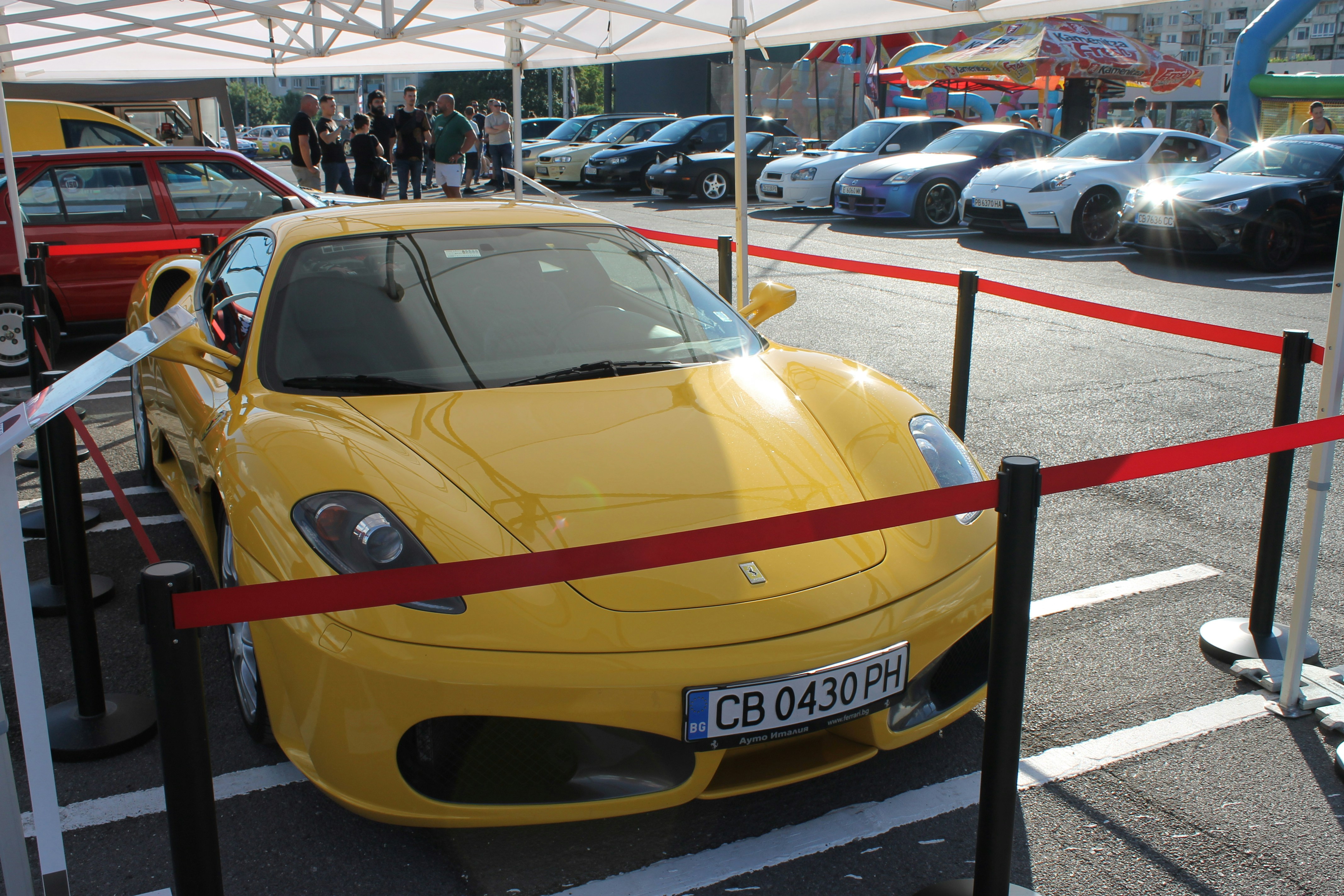 A striking yellow sports car showcased at an event, surrounded by barriers and other vehicles in the background.