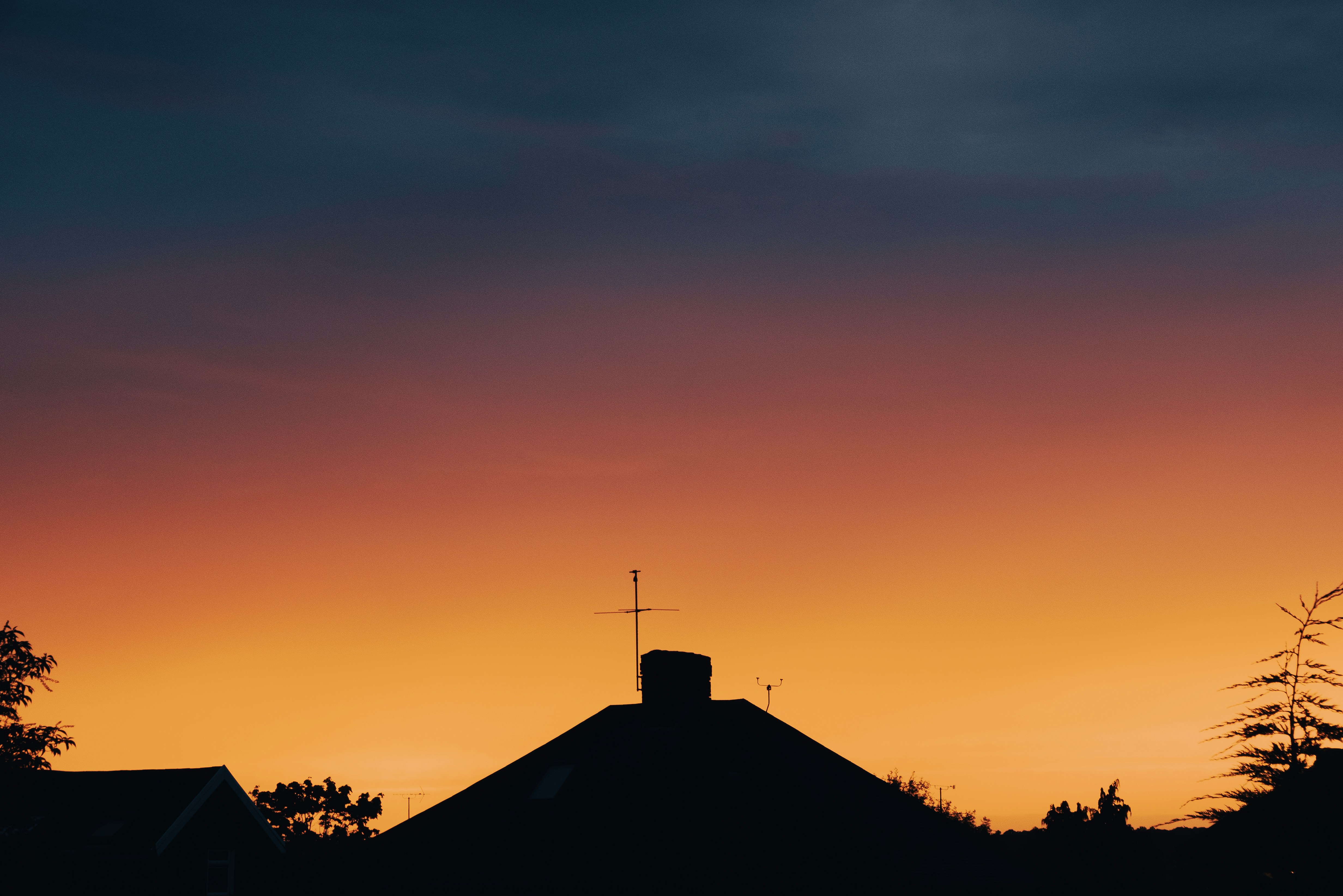 Silhouetted rooftops against a gradient sky transitioning from deep orange to twilight blue.
