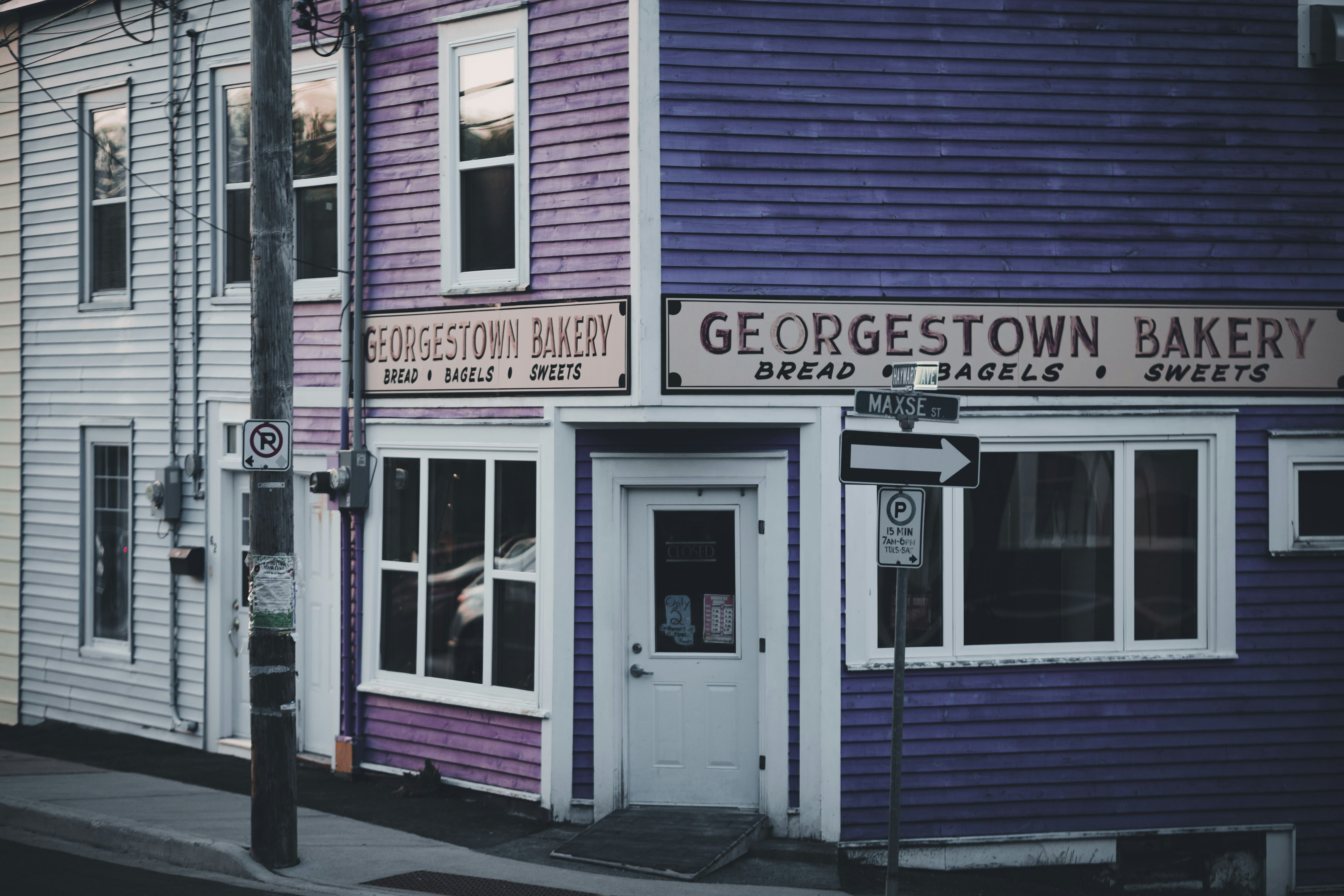 Quaint bakery exterior featuring purple siding and a welcoming entrance, showcasing its name and offerings. The scene captures the essence of a local community hub.