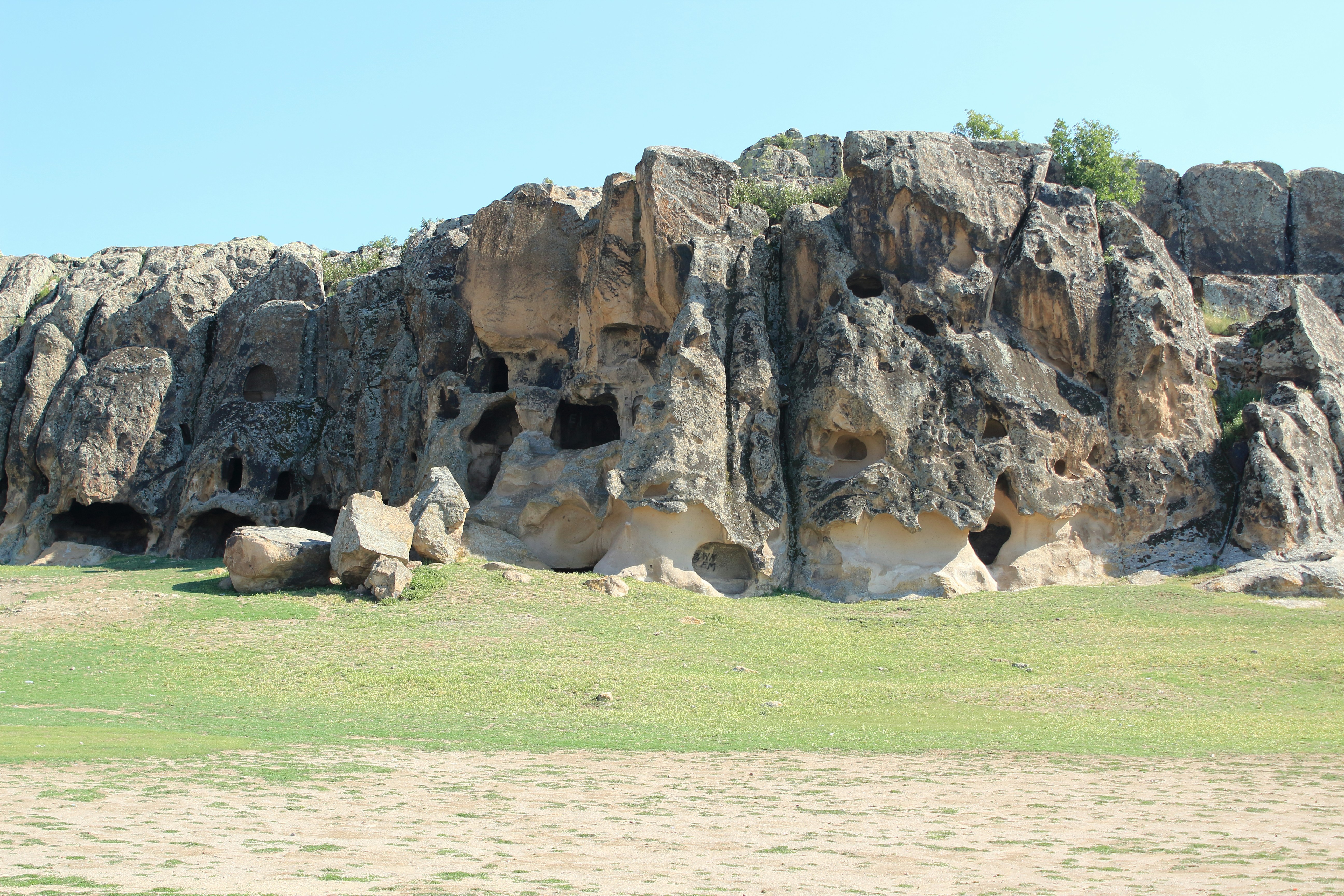 Weathered rock formations with natural cavities and greenery at the base, showcasing geological history.