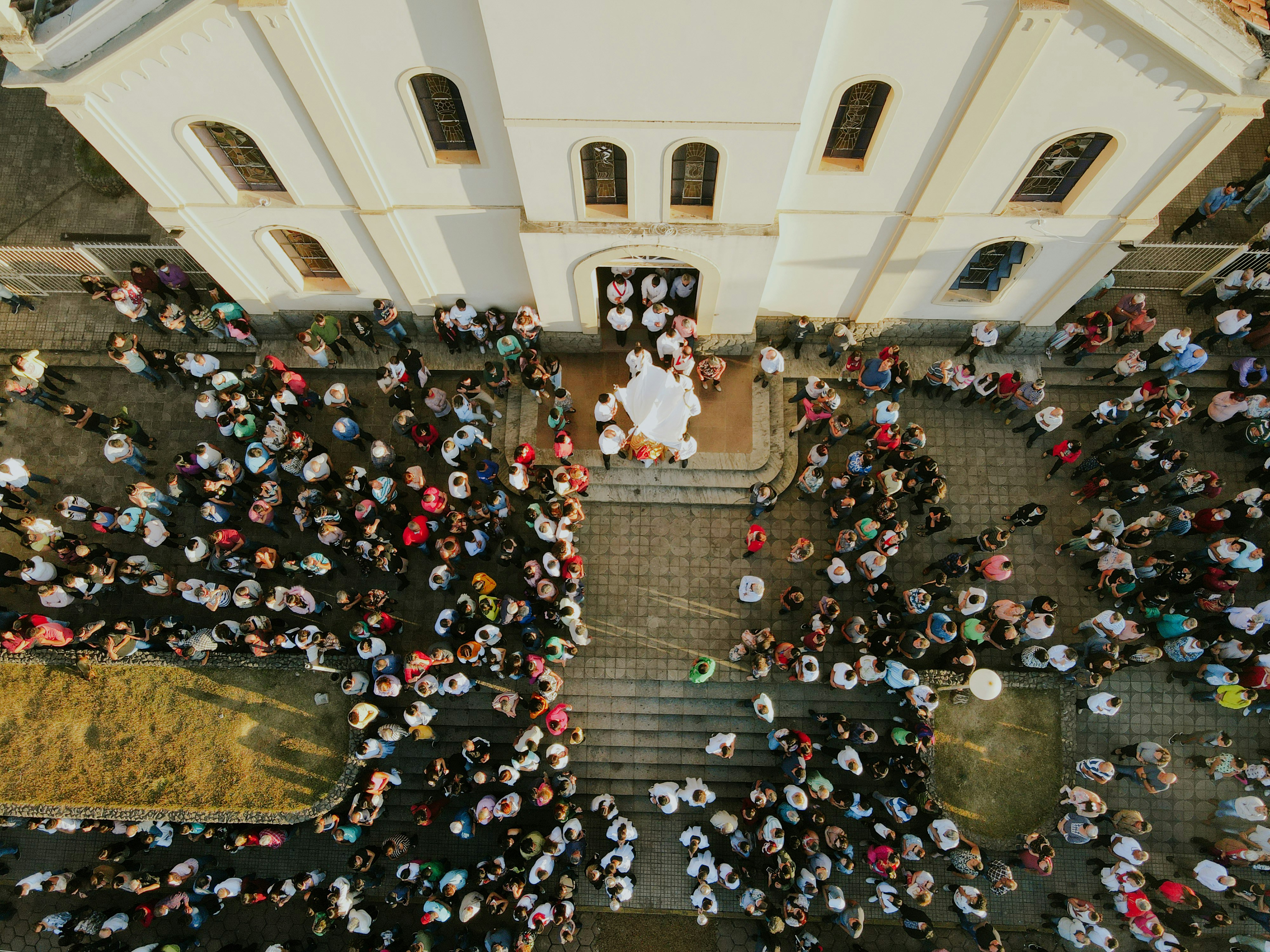 Aerial view of a large crowd gathered outside a white building with a staircase.