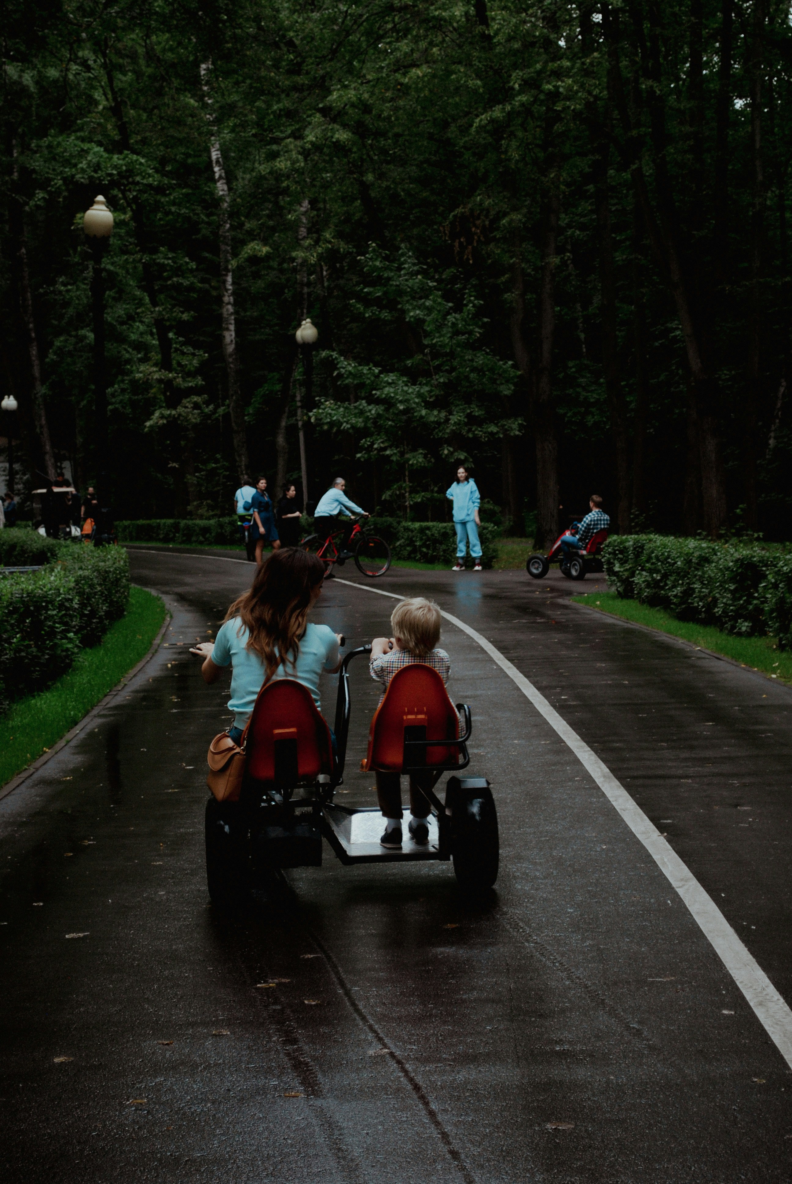 Two Children on a Red Wagon Glide Along a Rain-Washed Park Path