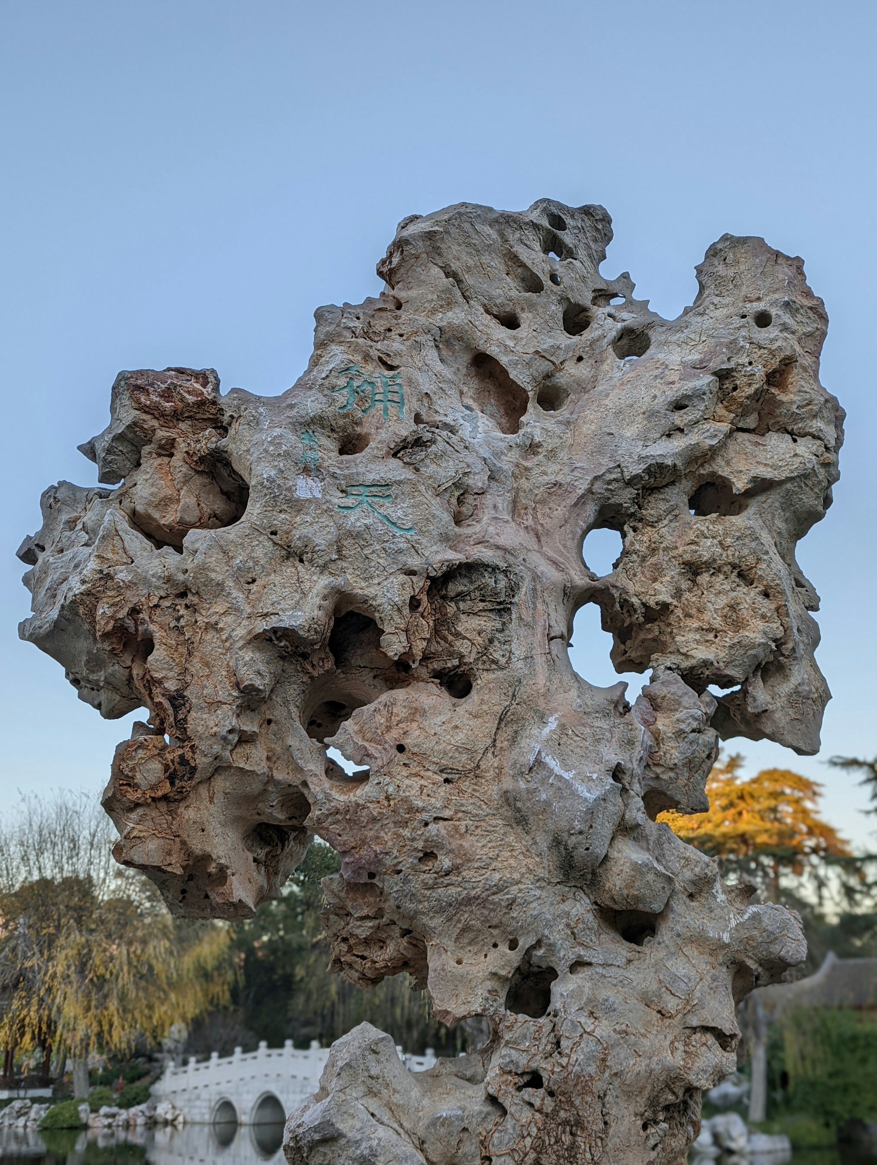 Perforated Sentinel: Weathered Stone with Green Script in a Tranquil Garden