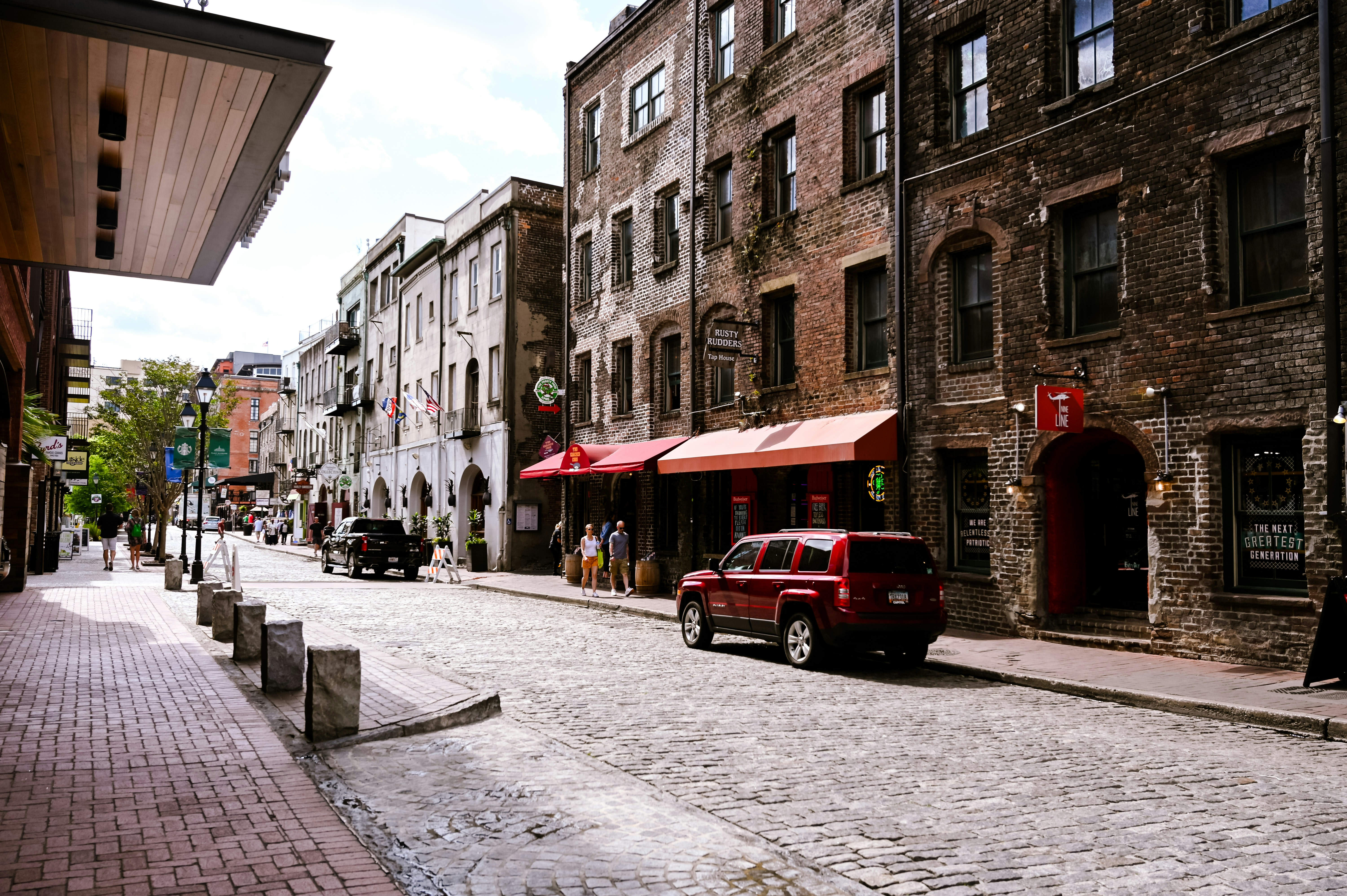 Cobblestone Street Between Brick Facades with Red SUV on a Quiet Day