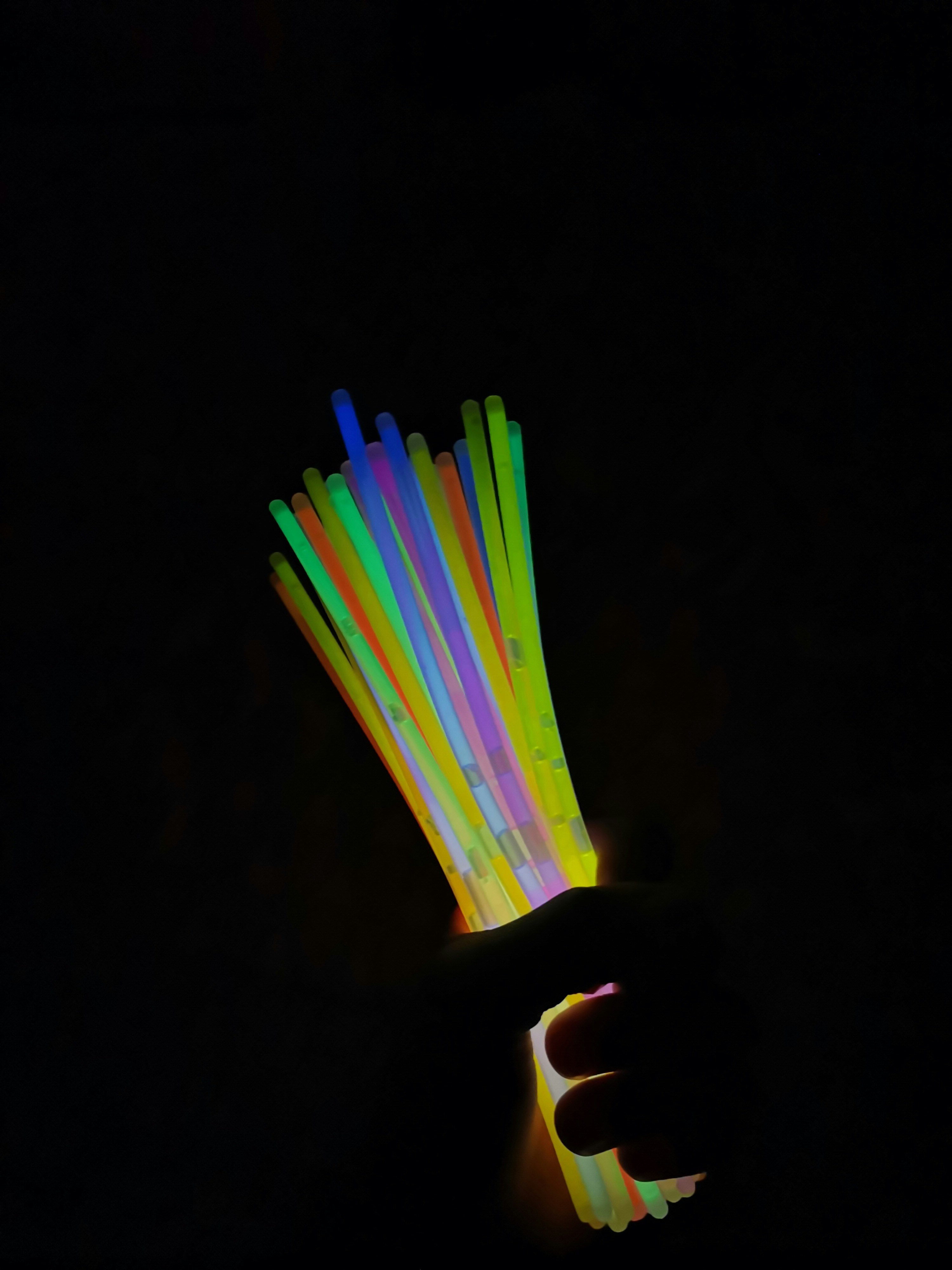 Hand holding a bundle of glowing sticks radiating vibrant colors against a dark background.