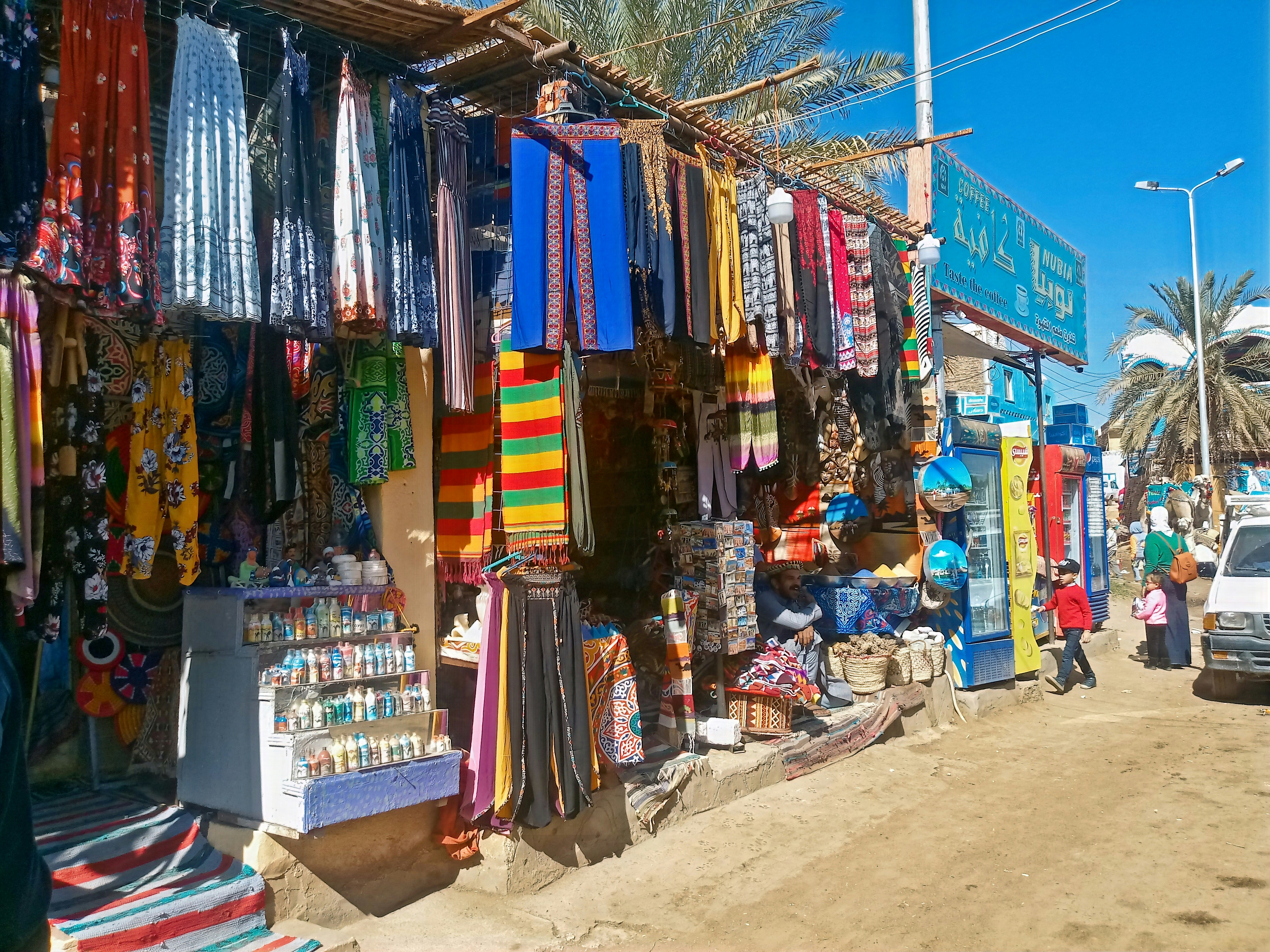 Vibrant textiles hanging outside a bustling market stall under a clear blue sky.