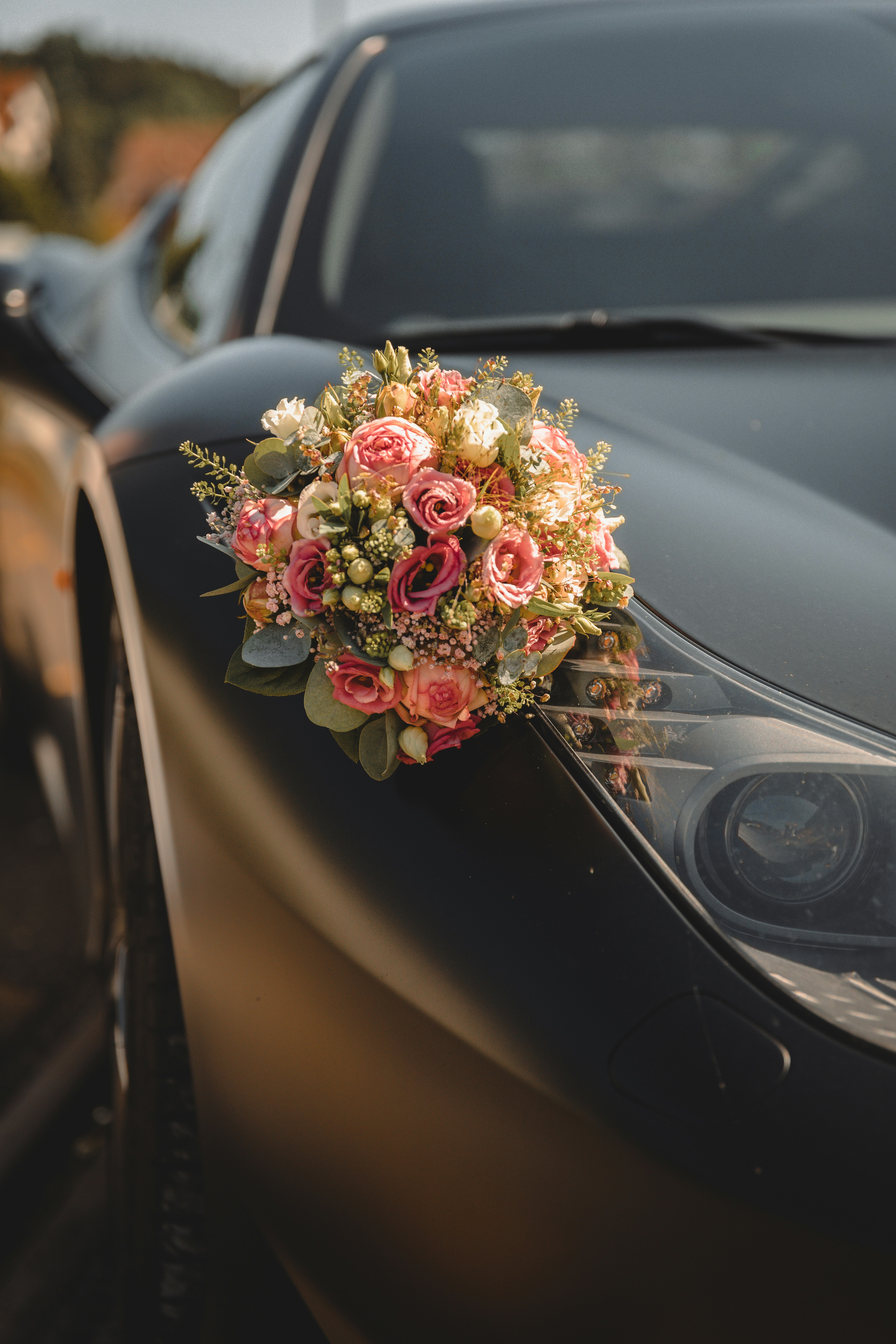 A vibrant bouquet of pink roses and greenery rests elegantly on the sleek hood of a luxury sports car, symbolizing the union of nature and automotive beauty.