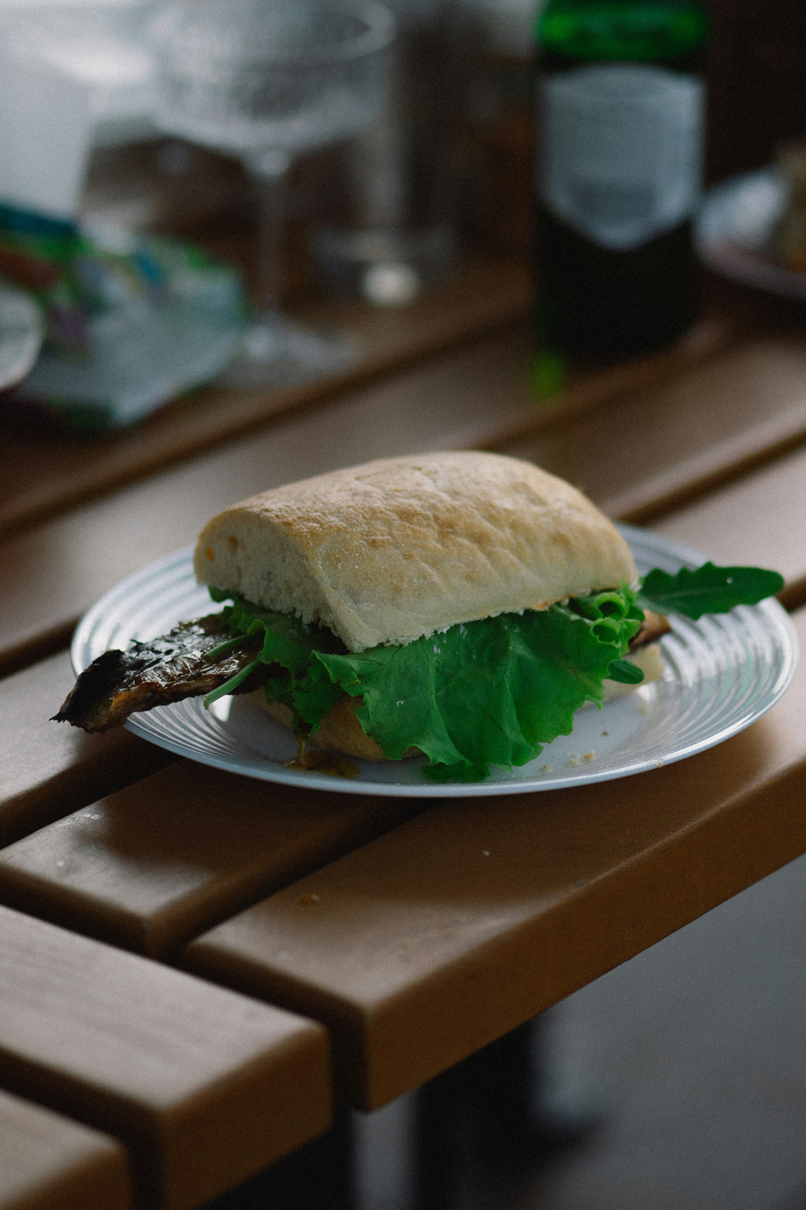 A sandwich featuring fresh lettuce and a savory filling, elegantly presented on a white plate atop a wooden table.