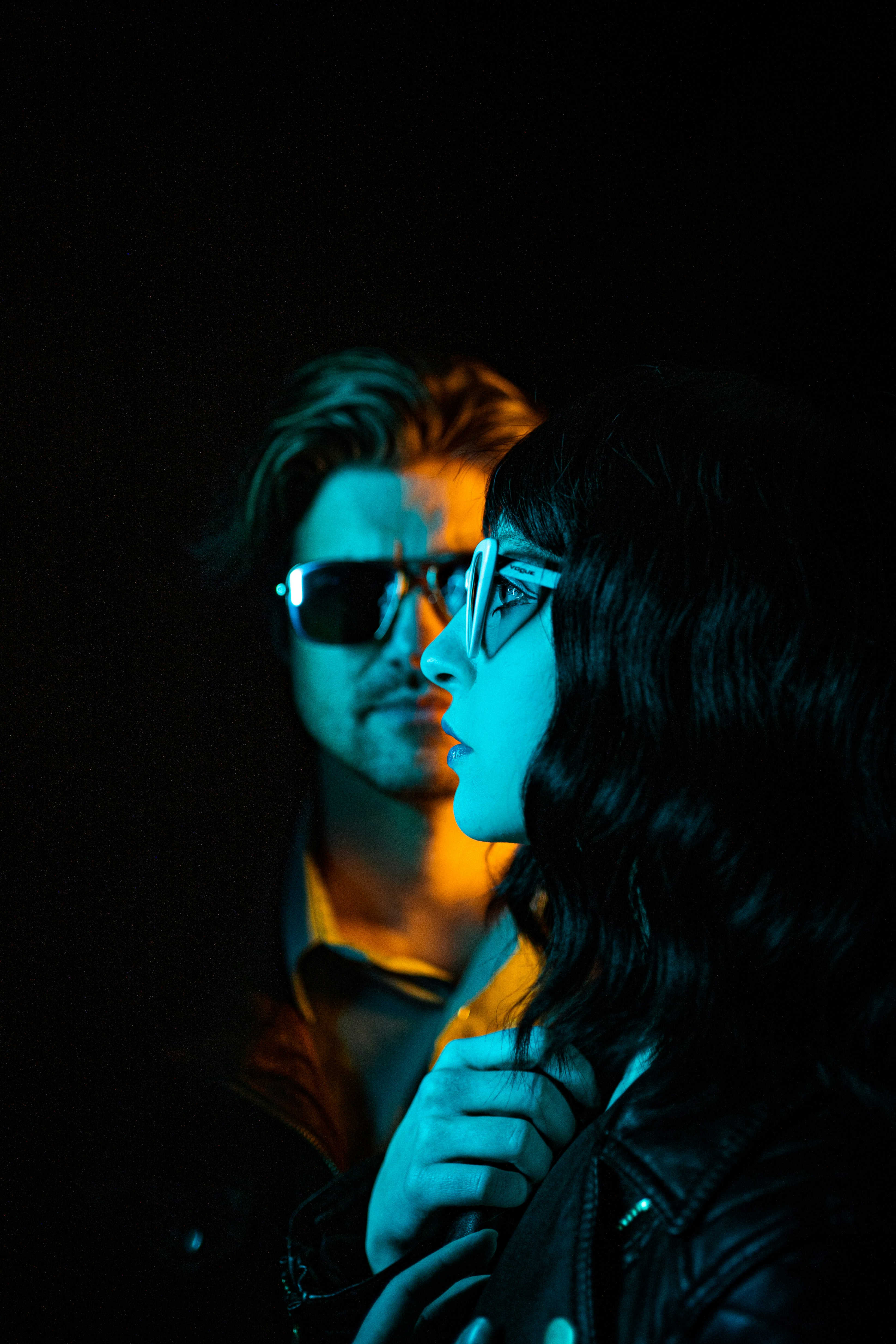 A striking portrait featuring two figures illuminated by contrasting neon lighting, showcasing a blend of intrigue and modern style.