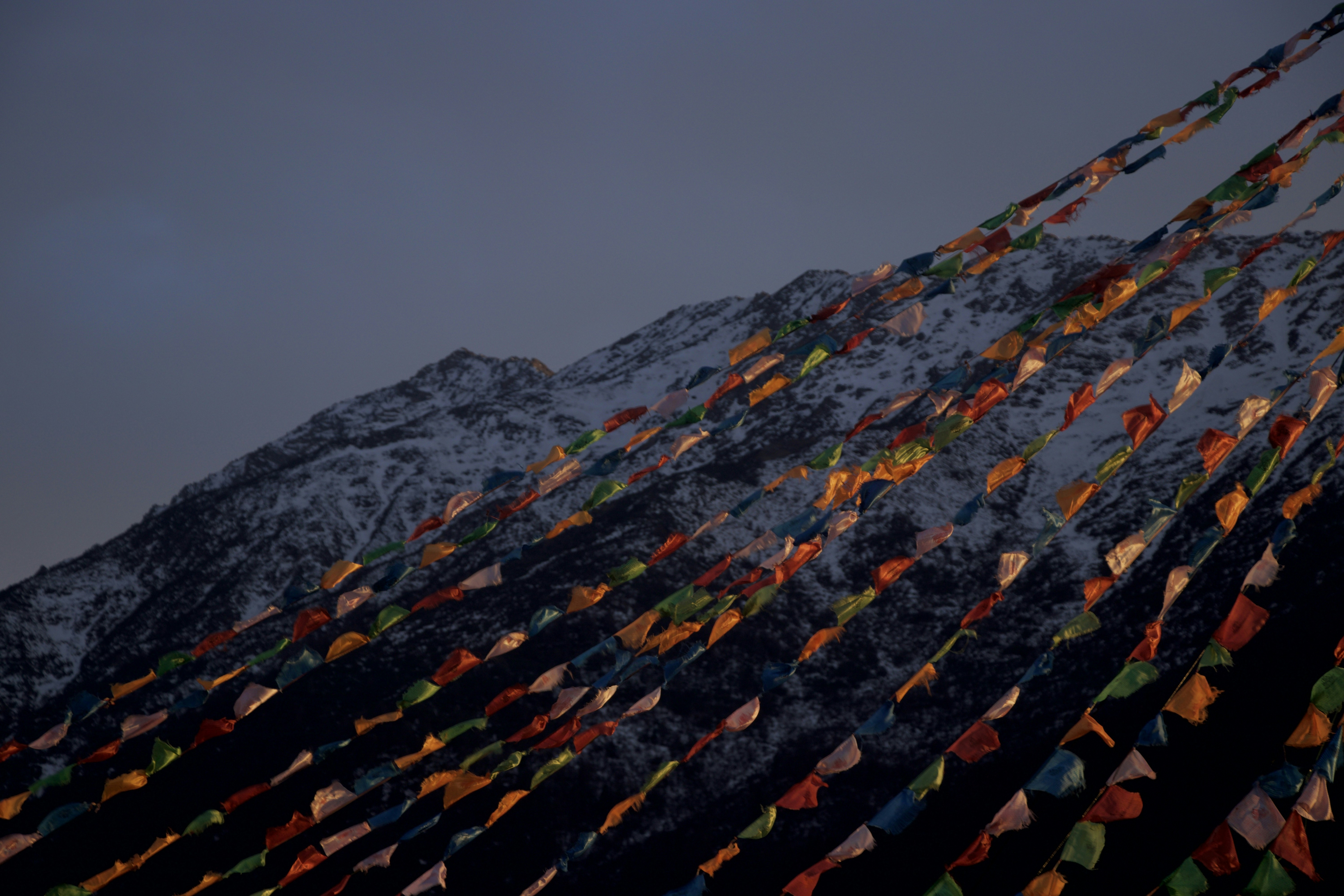 Colorful prayer flags fluttering against a backdrop of snow-capped mountains during twilight.