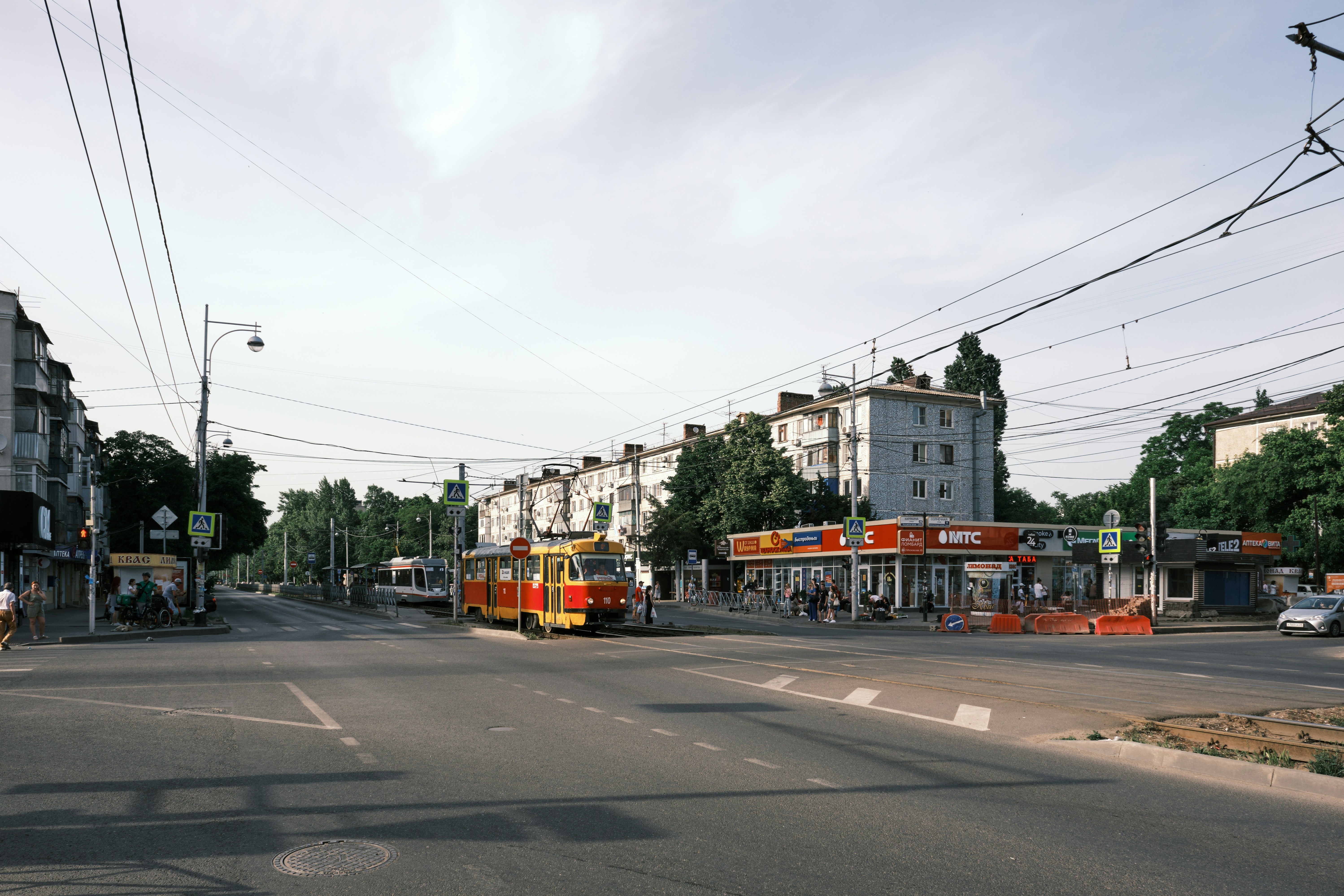 Tram navigating a quiet urban intersection surrounded by mid-century buildings and lush greenery.