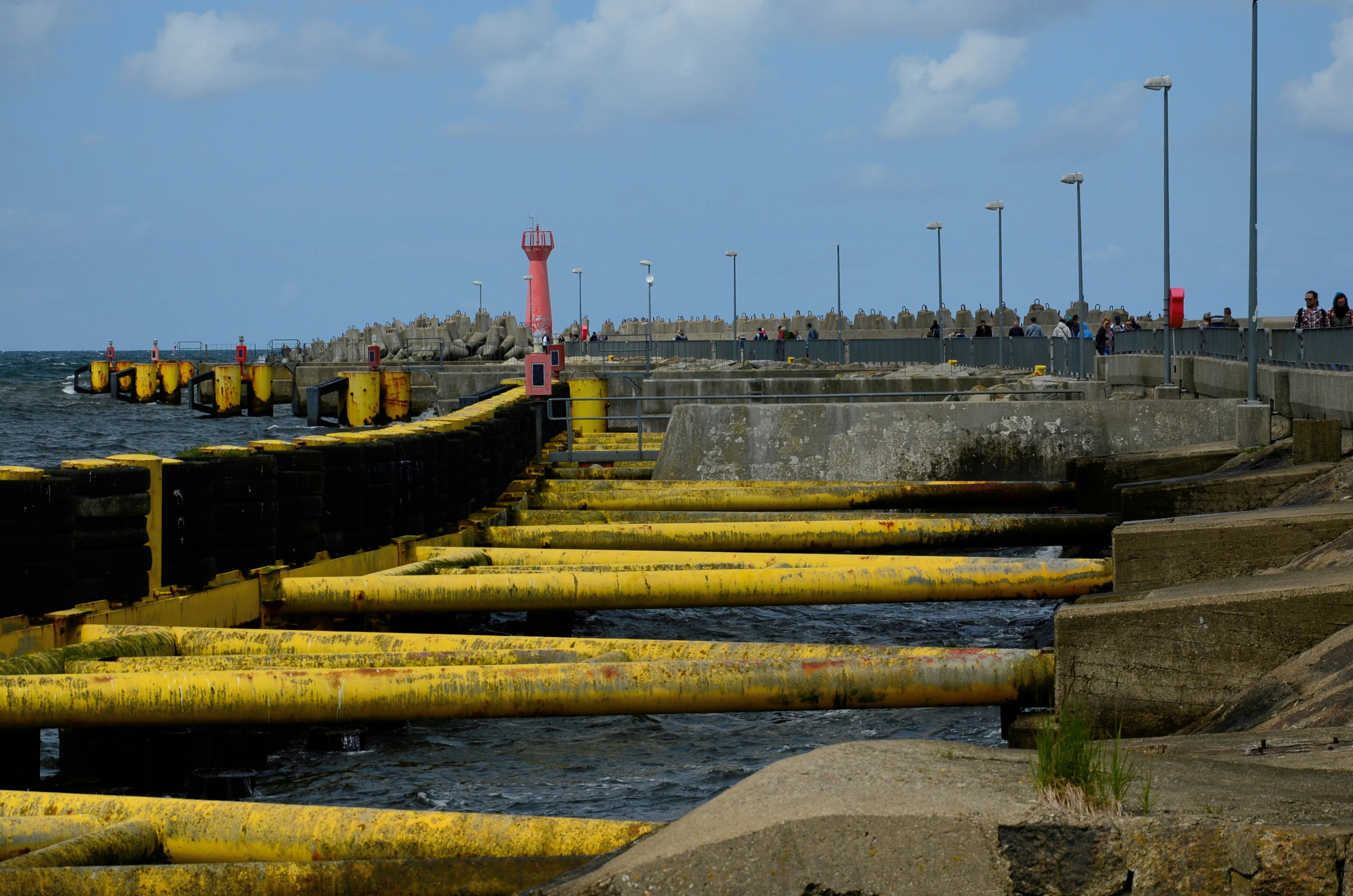 Yellow groynes lead the way to a seaside promenade under a red beacon