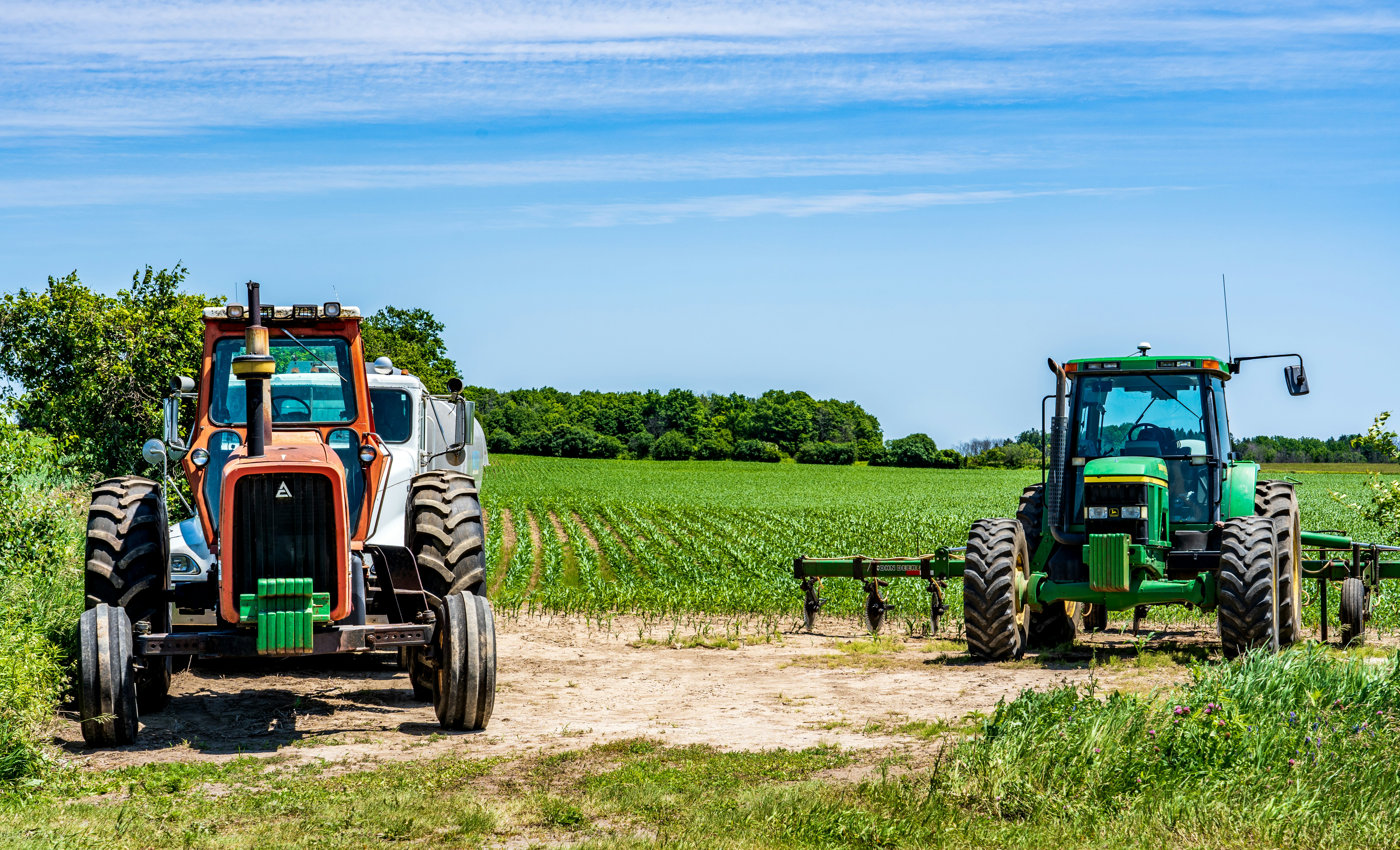 Two tractors parked at a rural crossroads, surrounded by lush green fields under a clear blue sky.