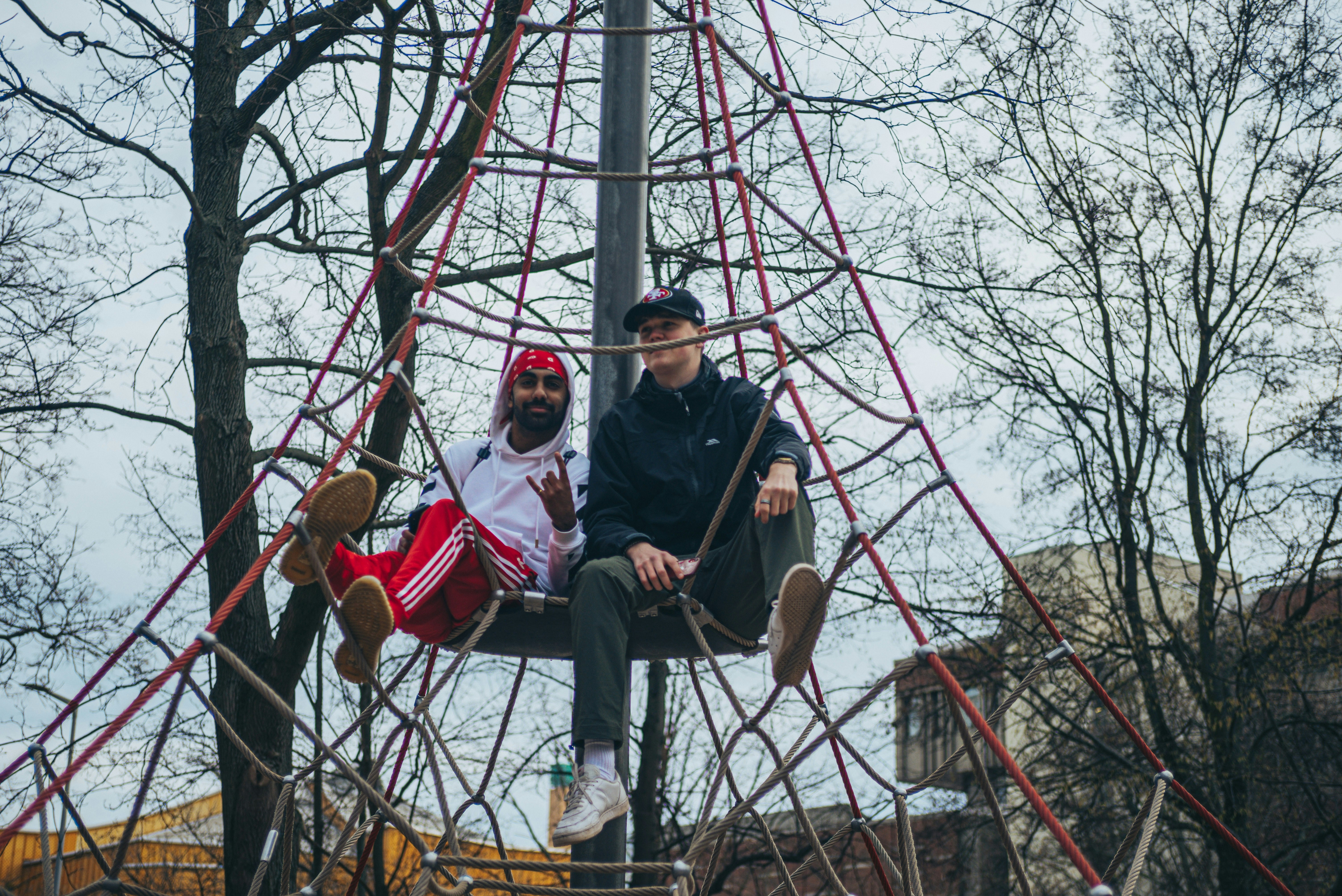 Rope-Net Rendezvous: Two friends perched on a suspended net beneath bare branches