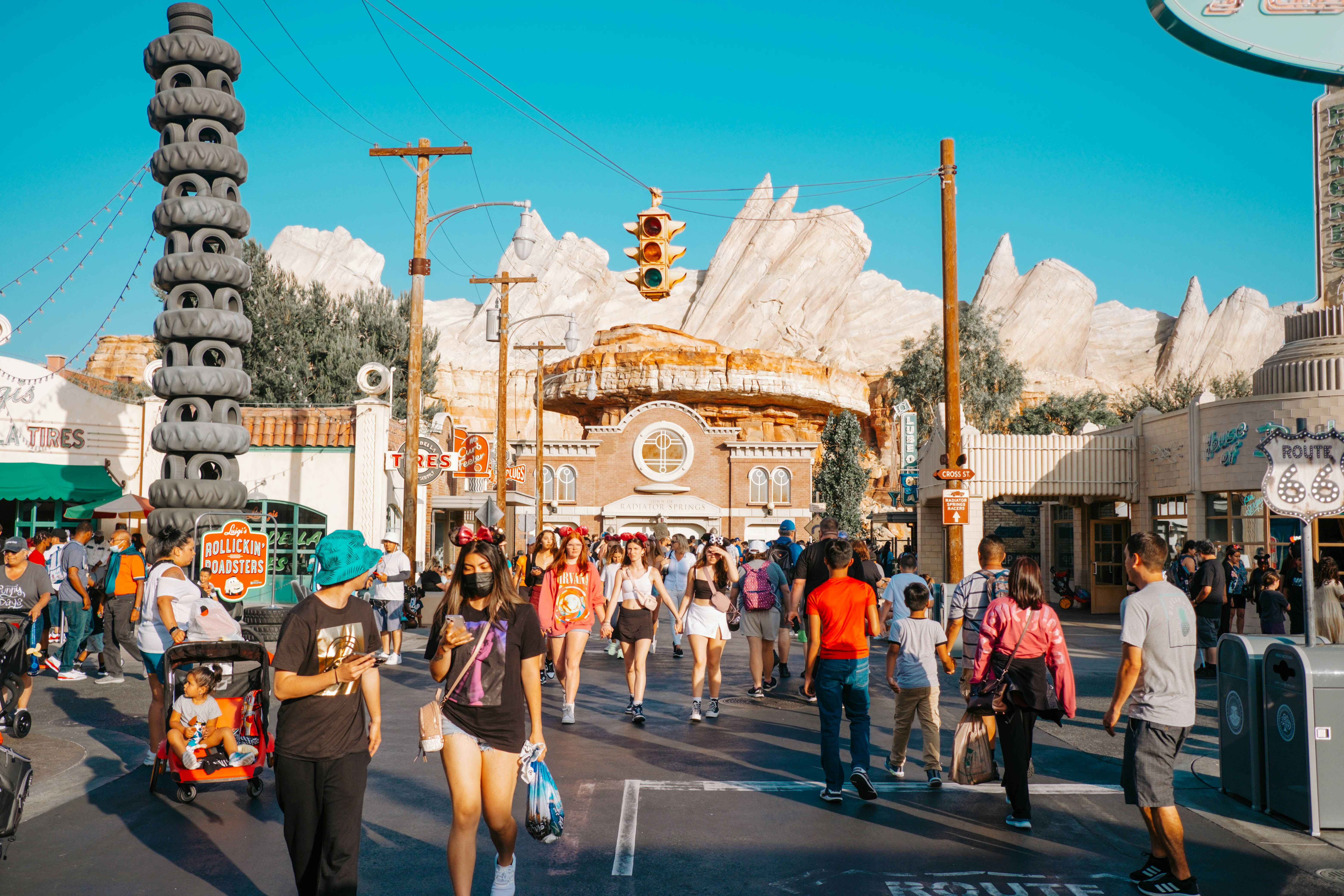 Crowd of people crossing a lively theme park street under a clear blue sky.