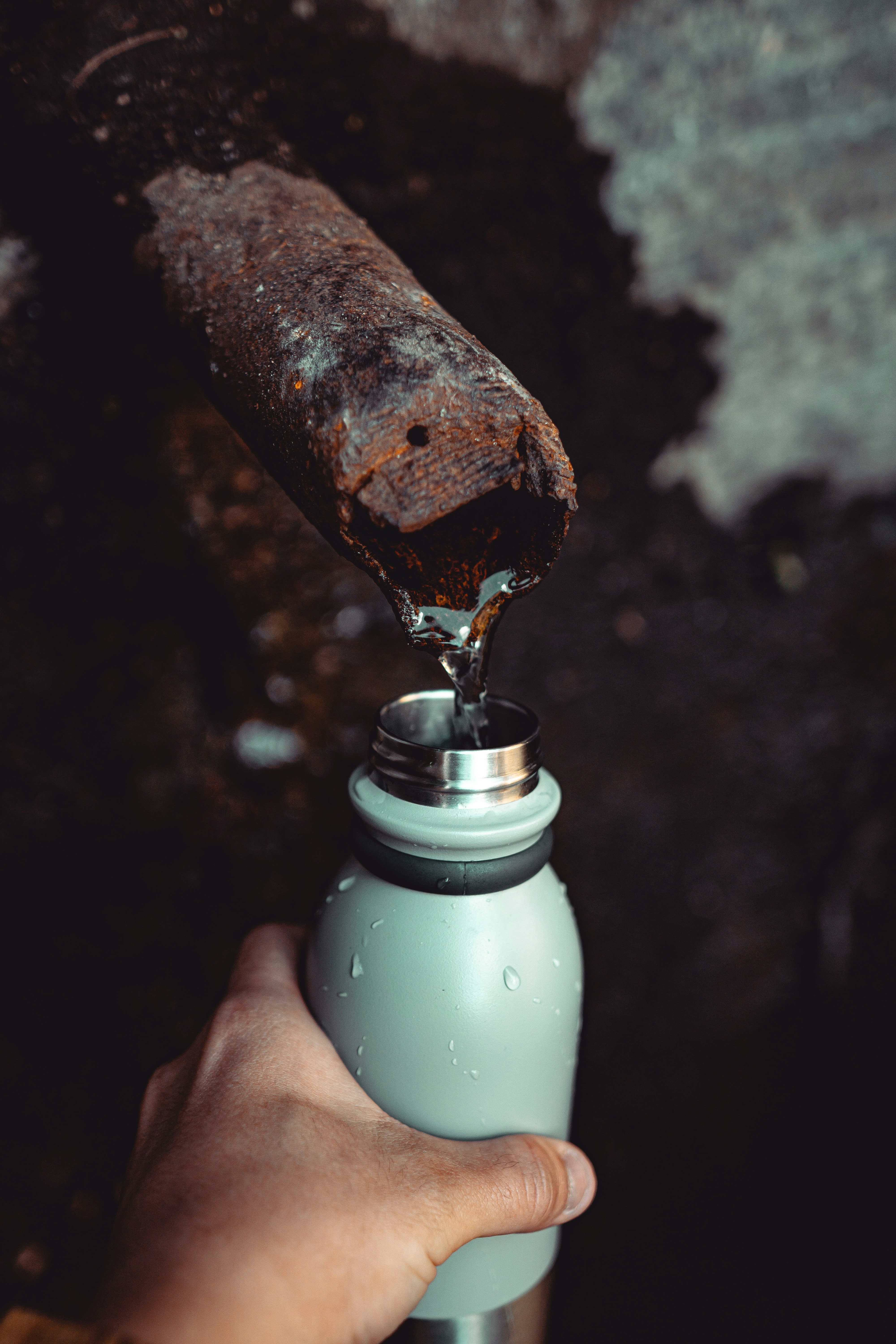 A hand holding a small blue bottle with a brown liquid coming out of it ...