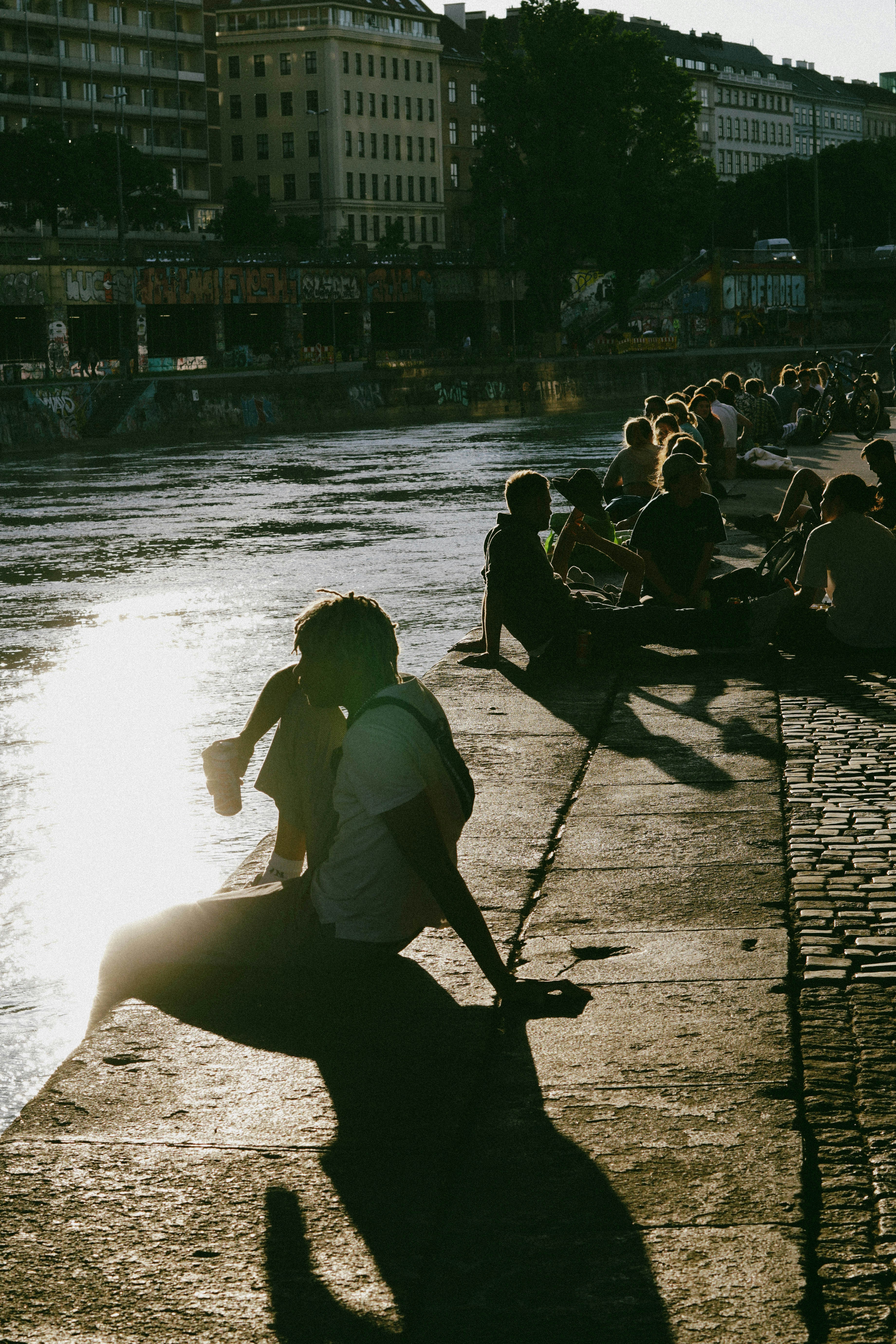Vienna Streets | a group of people sitting on benches by a river