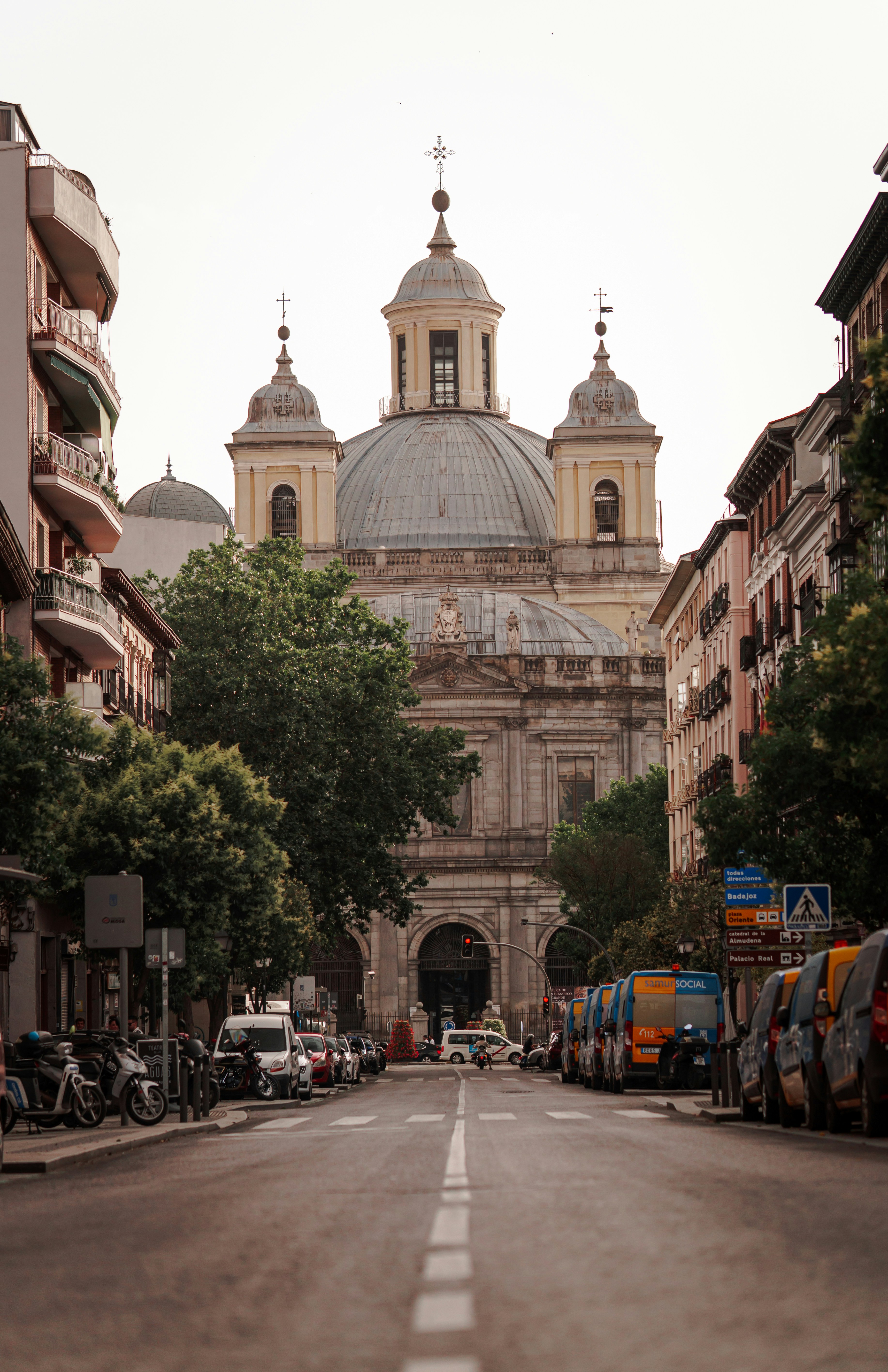Historic cathedral framed by a symmetrical street view, with trees and parked cars lining the road.