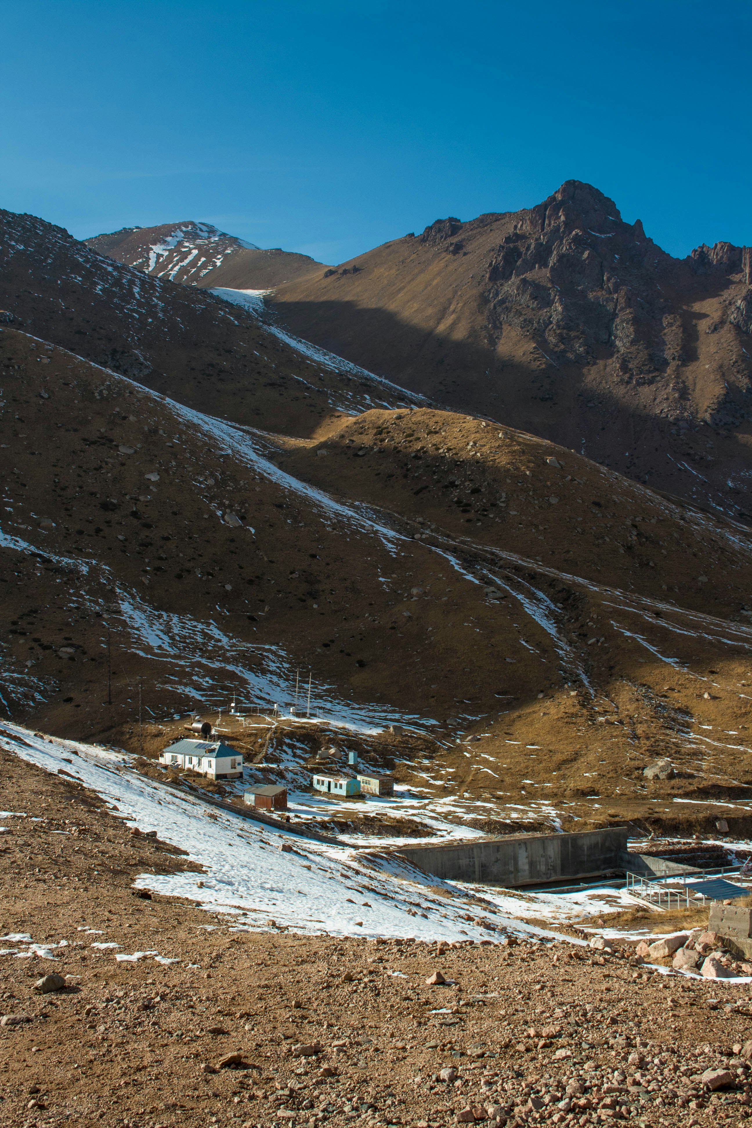 Snow-dusted landscape showcasing a remote settlement nestled in the mountains, with rugged peaks in the background. The scene captures the serenity of high-altitude living.