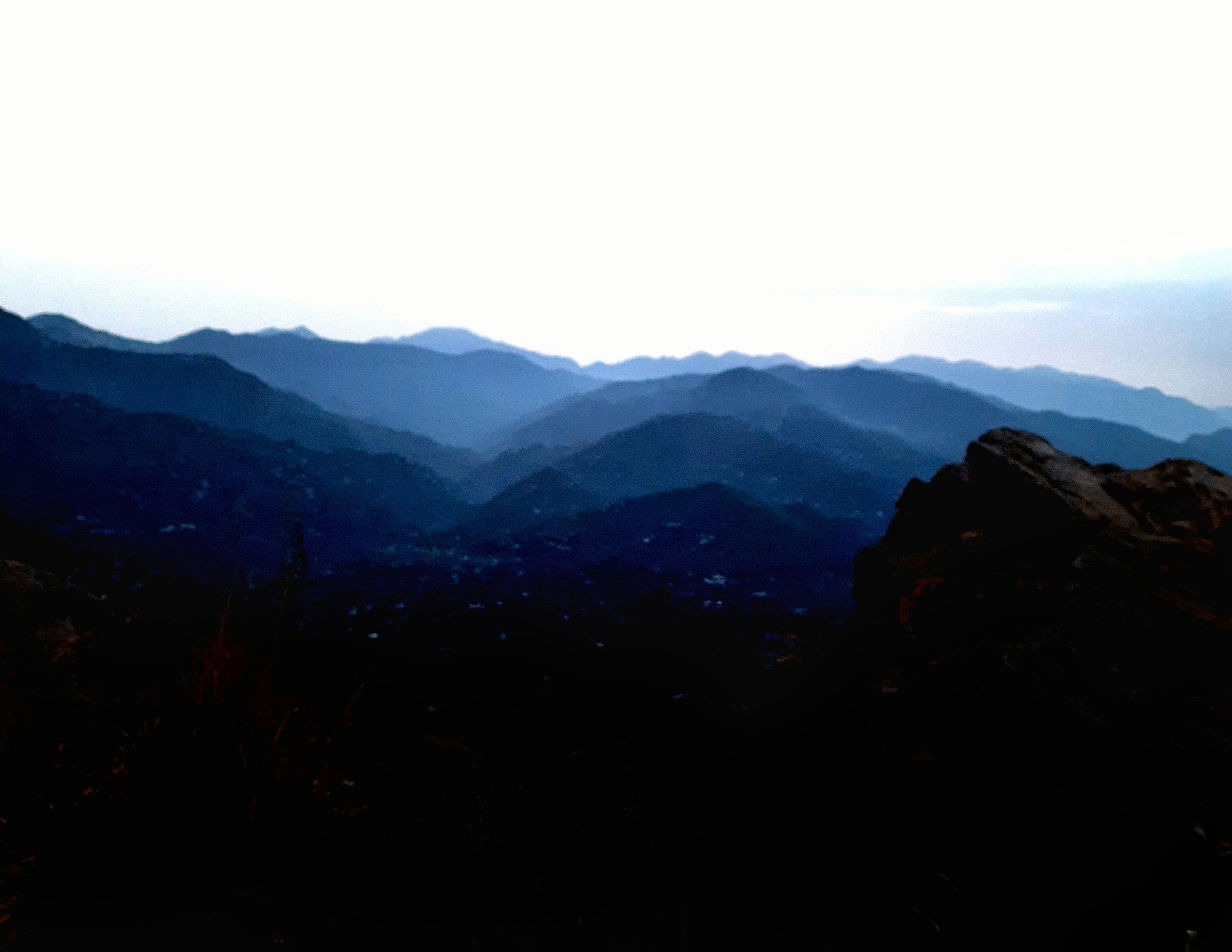 Layered mountain ranges fade into the horizon under a softly lit sky, creating a serene atmosphere. The image captures the transition from day to night.