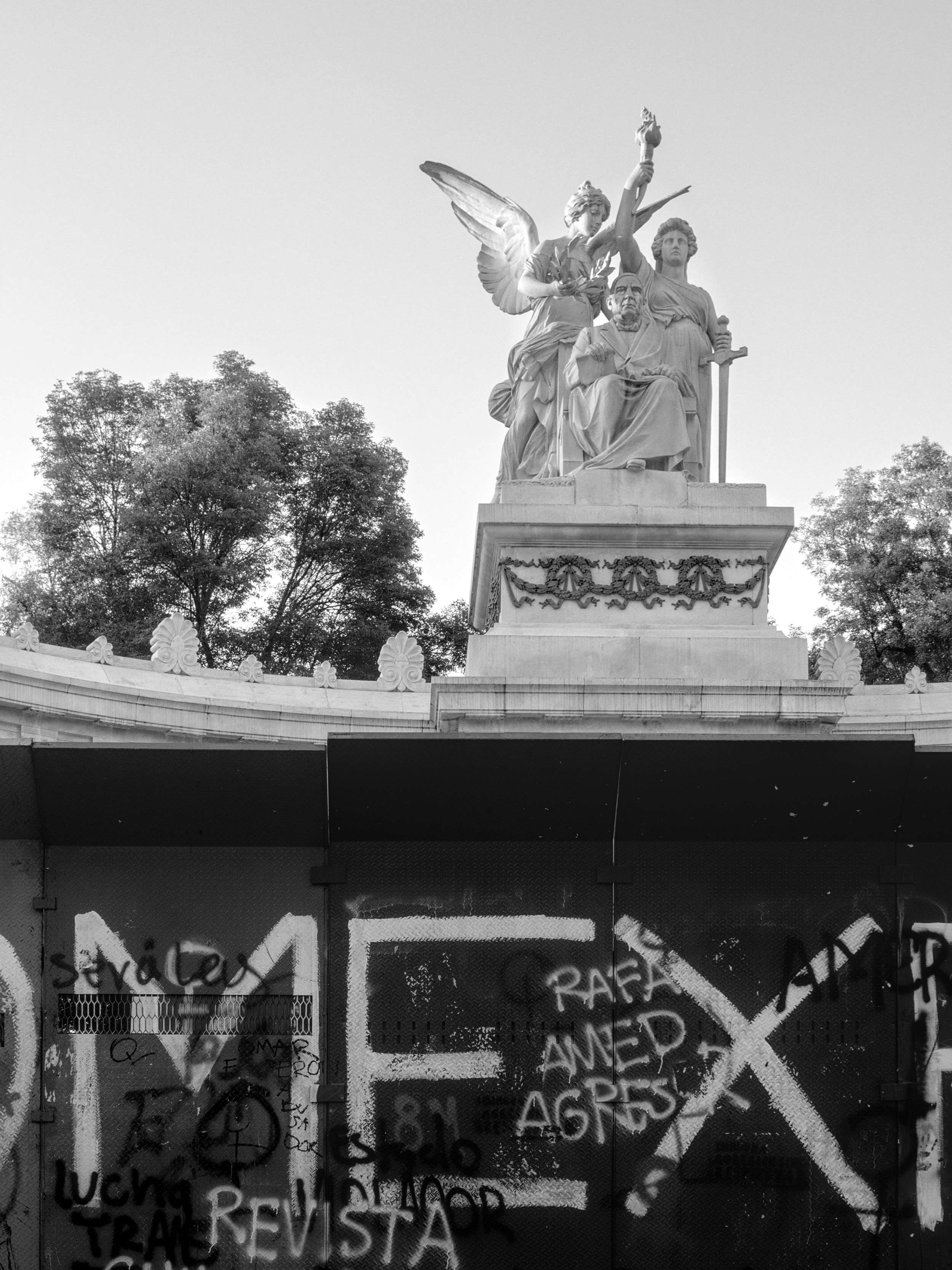 A grand statue depicting allegorical figures stands prominently, partially obscured by graffiti-covered walls, highlighting the contrast between art and urban culture.