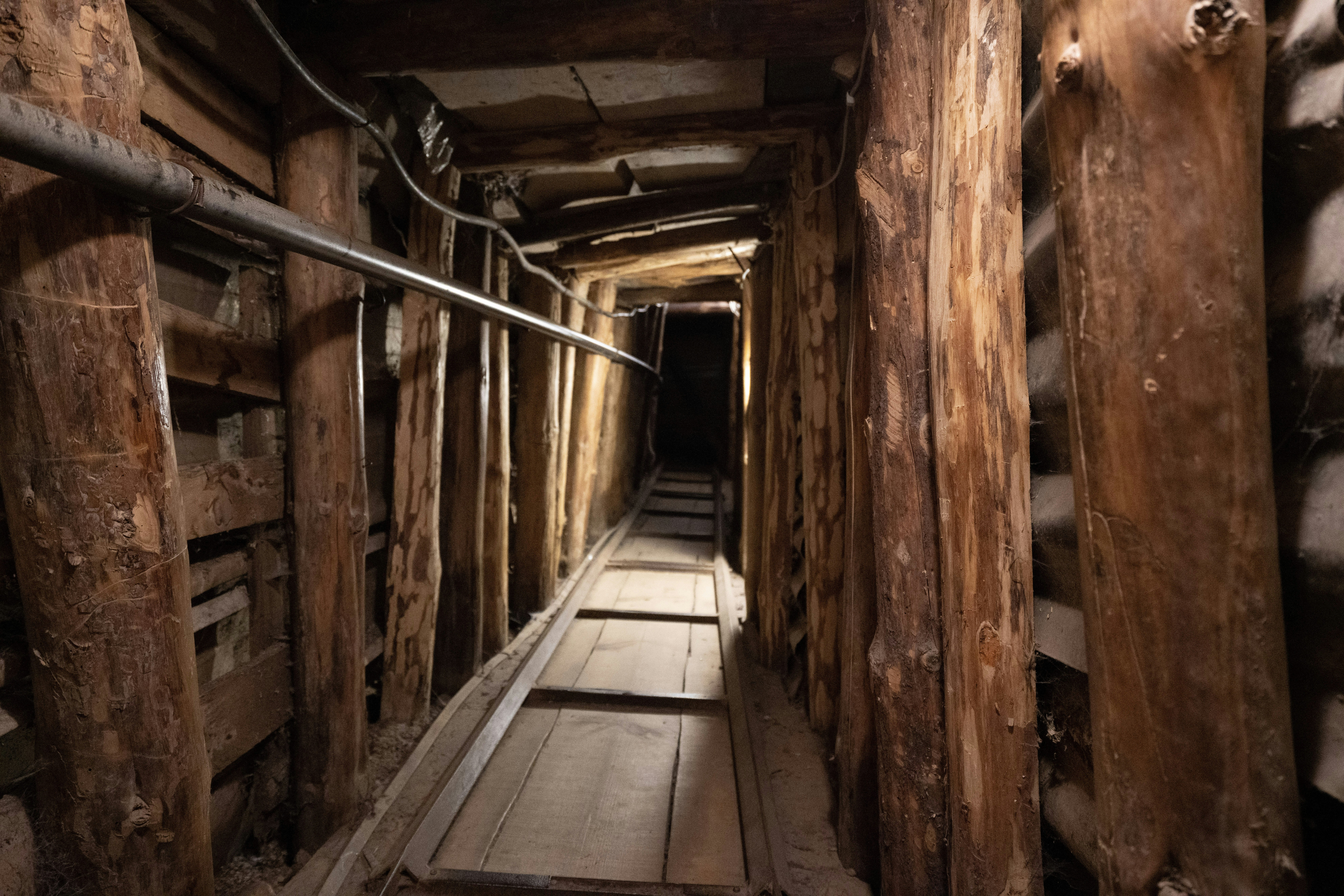 Wooden tunnel with exposed beams and dim lighting, leading into darkness.