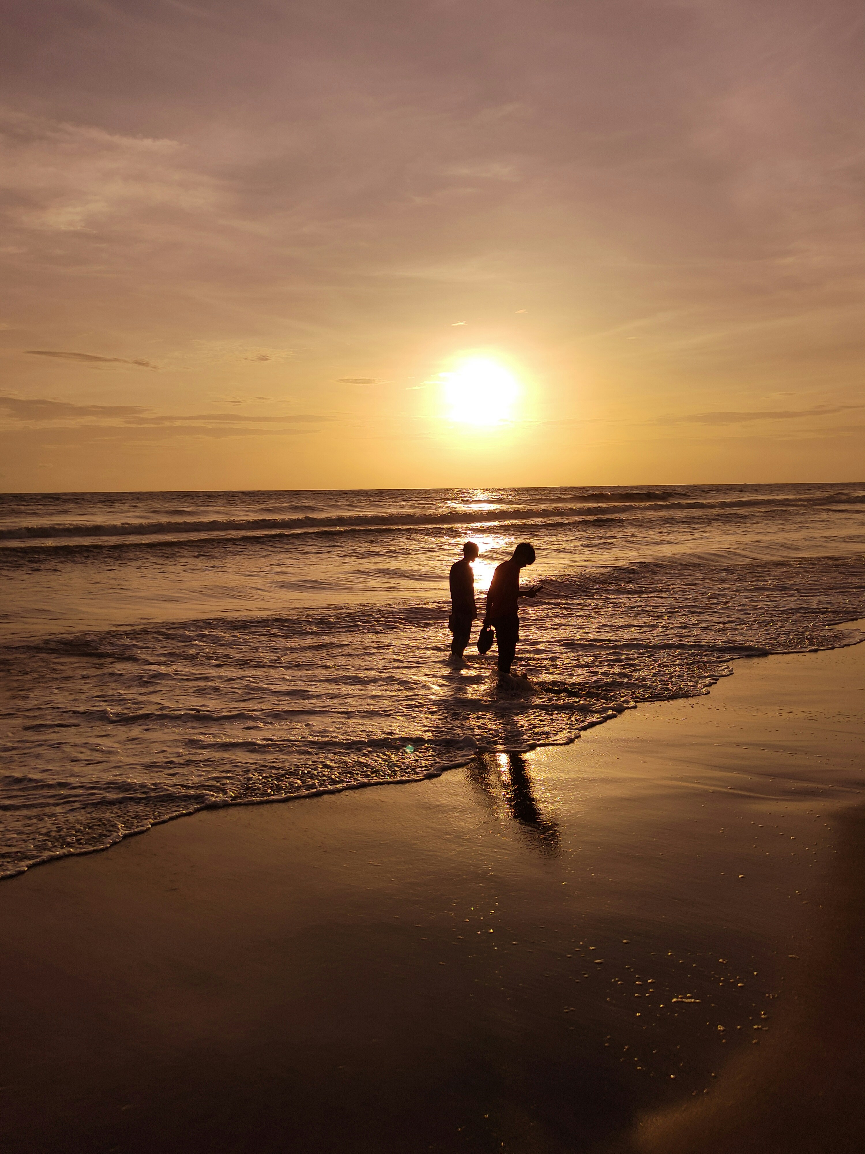 A couple of people standing on a beach with the sun setting photo ...