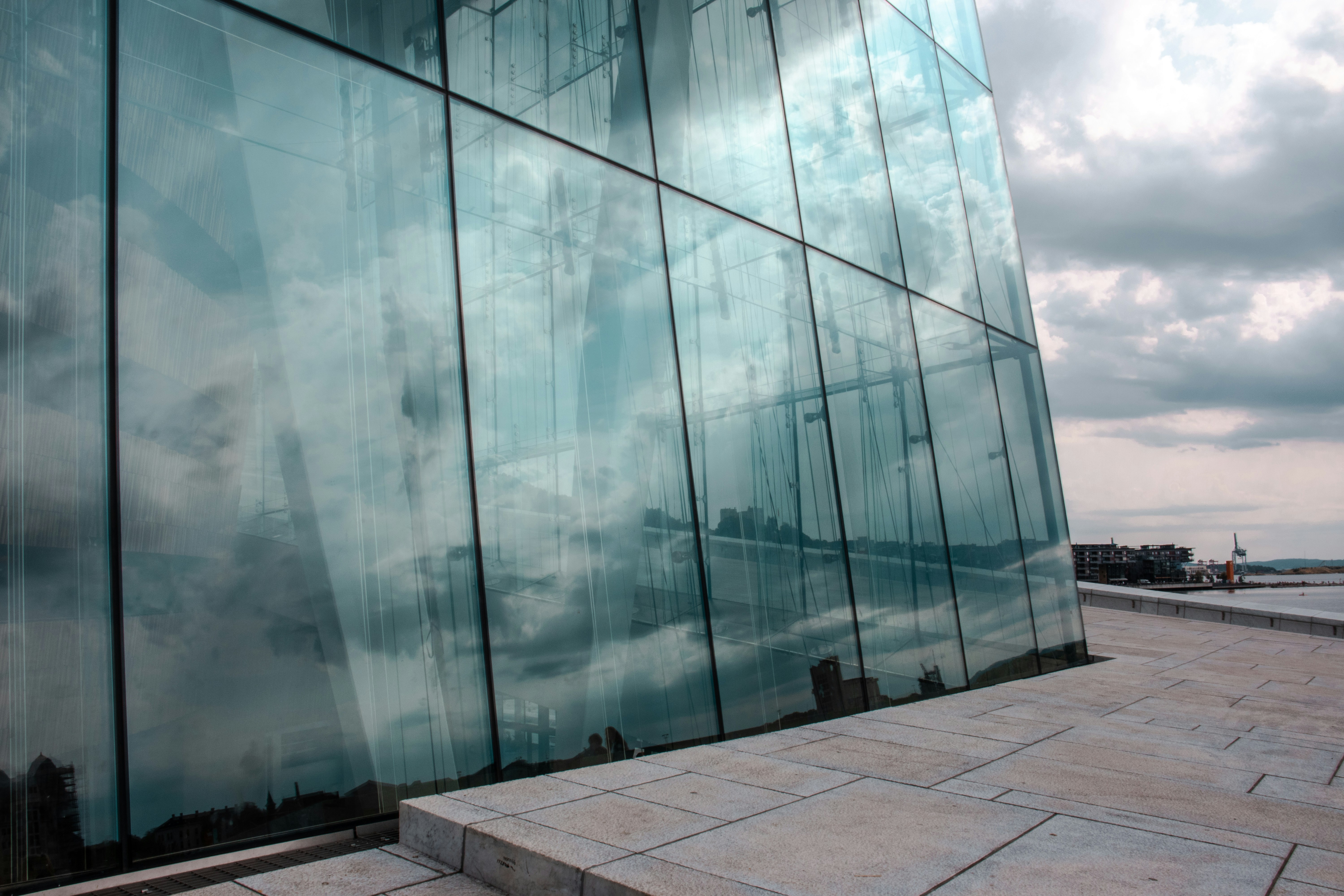 Reflective glass facade of a contemporary building, capturing the sky and surroundings in its surface. The architectural design emphasizes transparency and modern aesthetics.