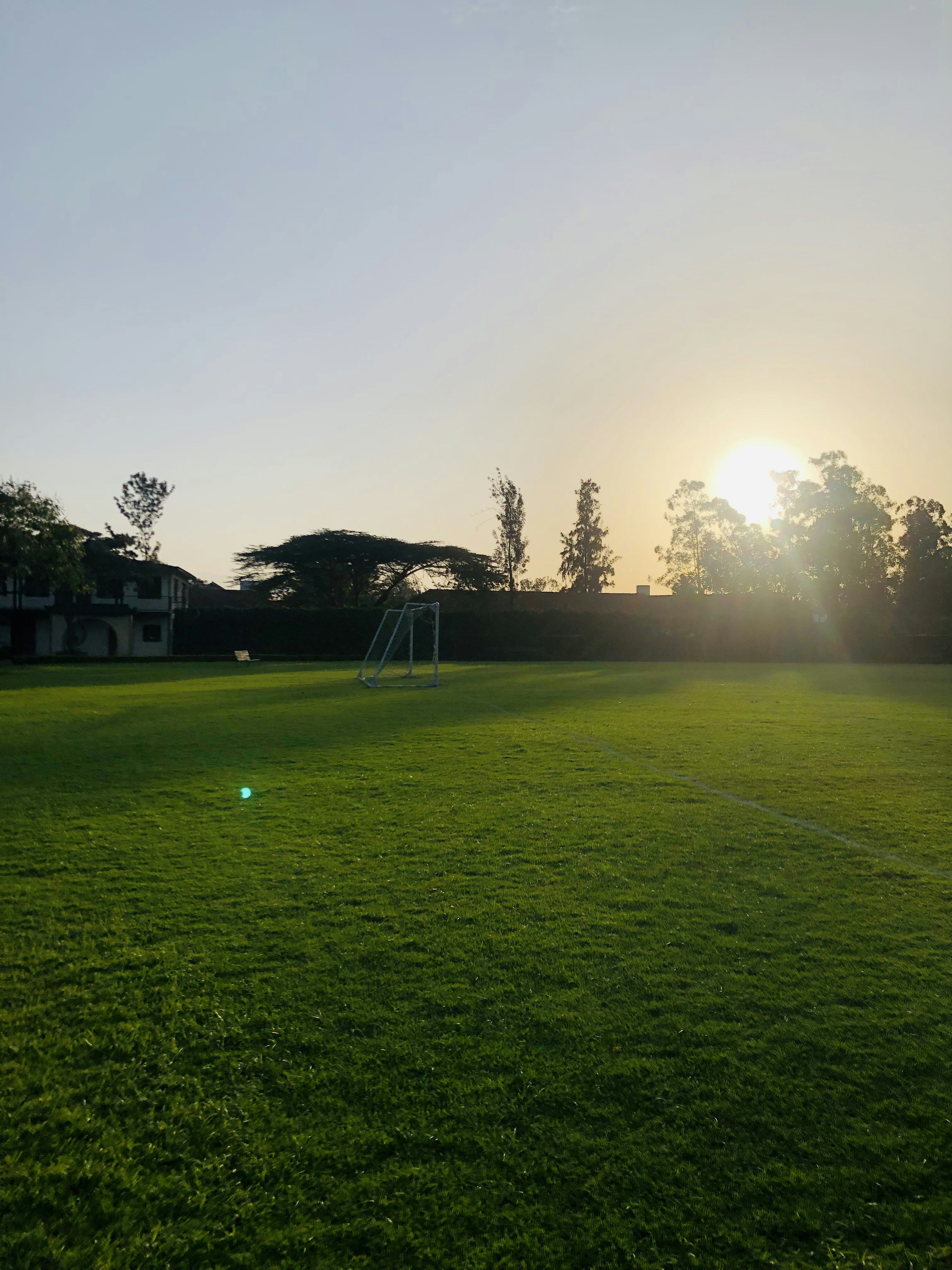 Soccer goalpost silhouetted against a vibrant sunset, with lush green grass filling the foreground.