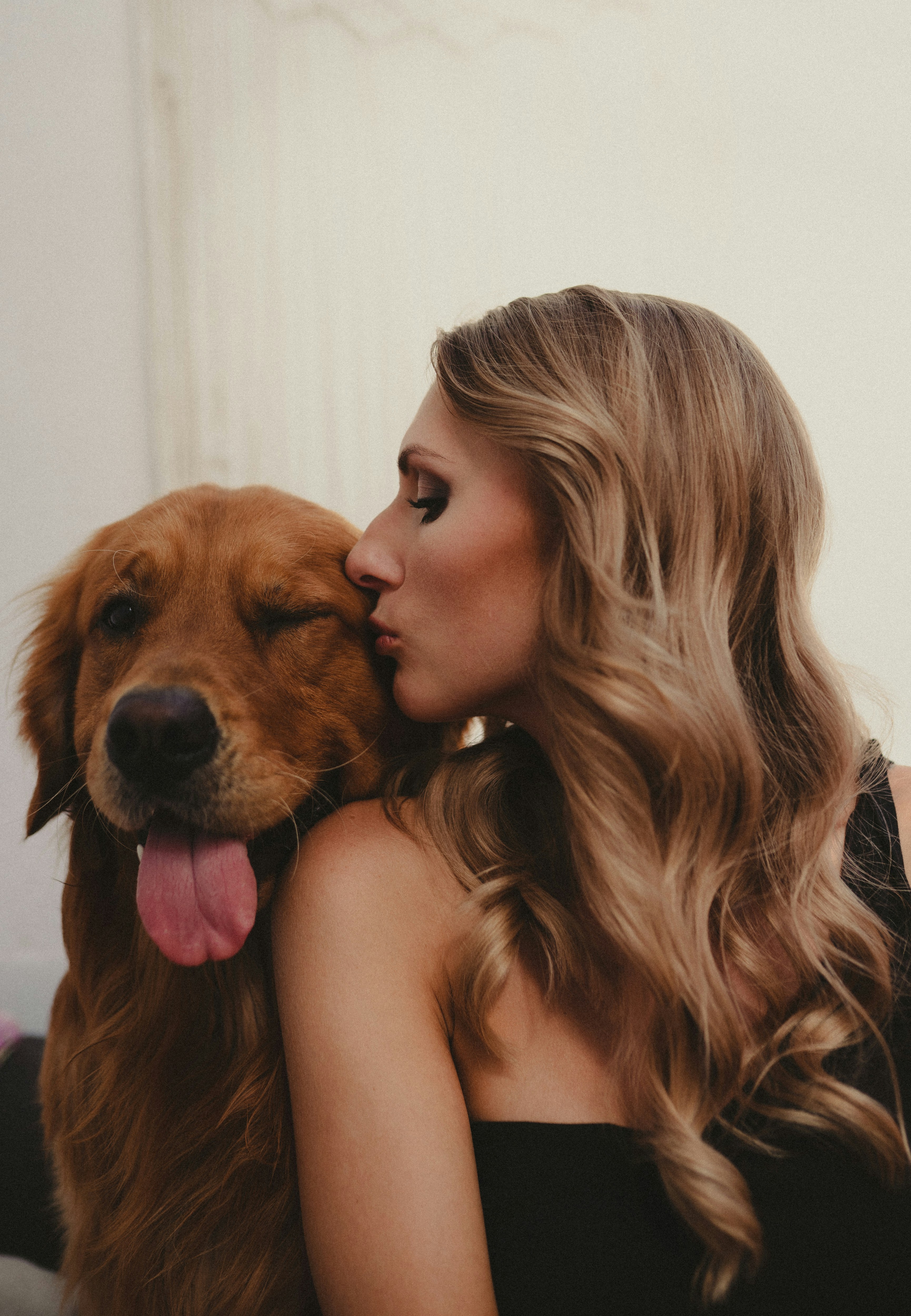 Woman sharing a tender kiss with a golden retriever, capturing an affectionate bond. Warm tones enhance the emotional connection.