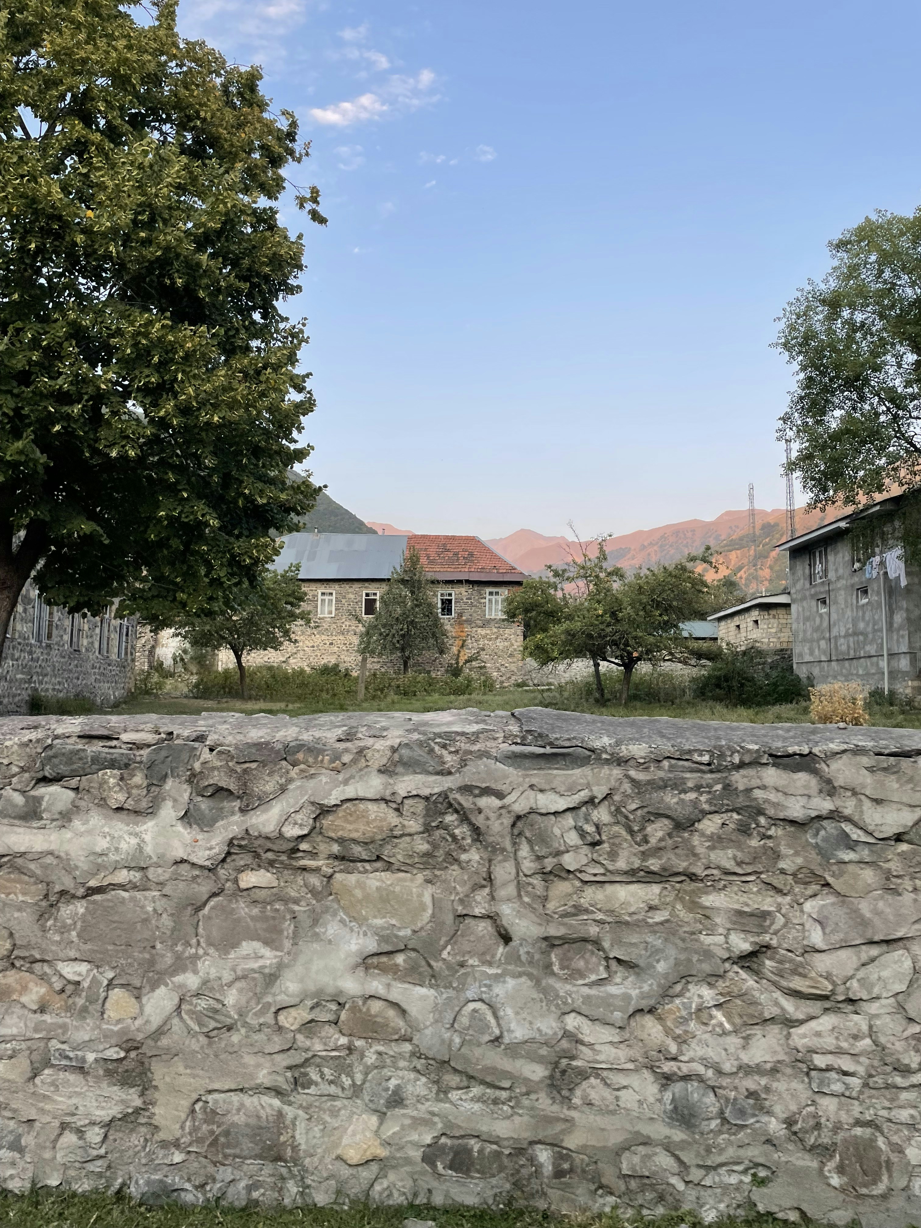 Foto Dinding batu dengan pagar batu dan pepohonan dan bangunan di latar ...