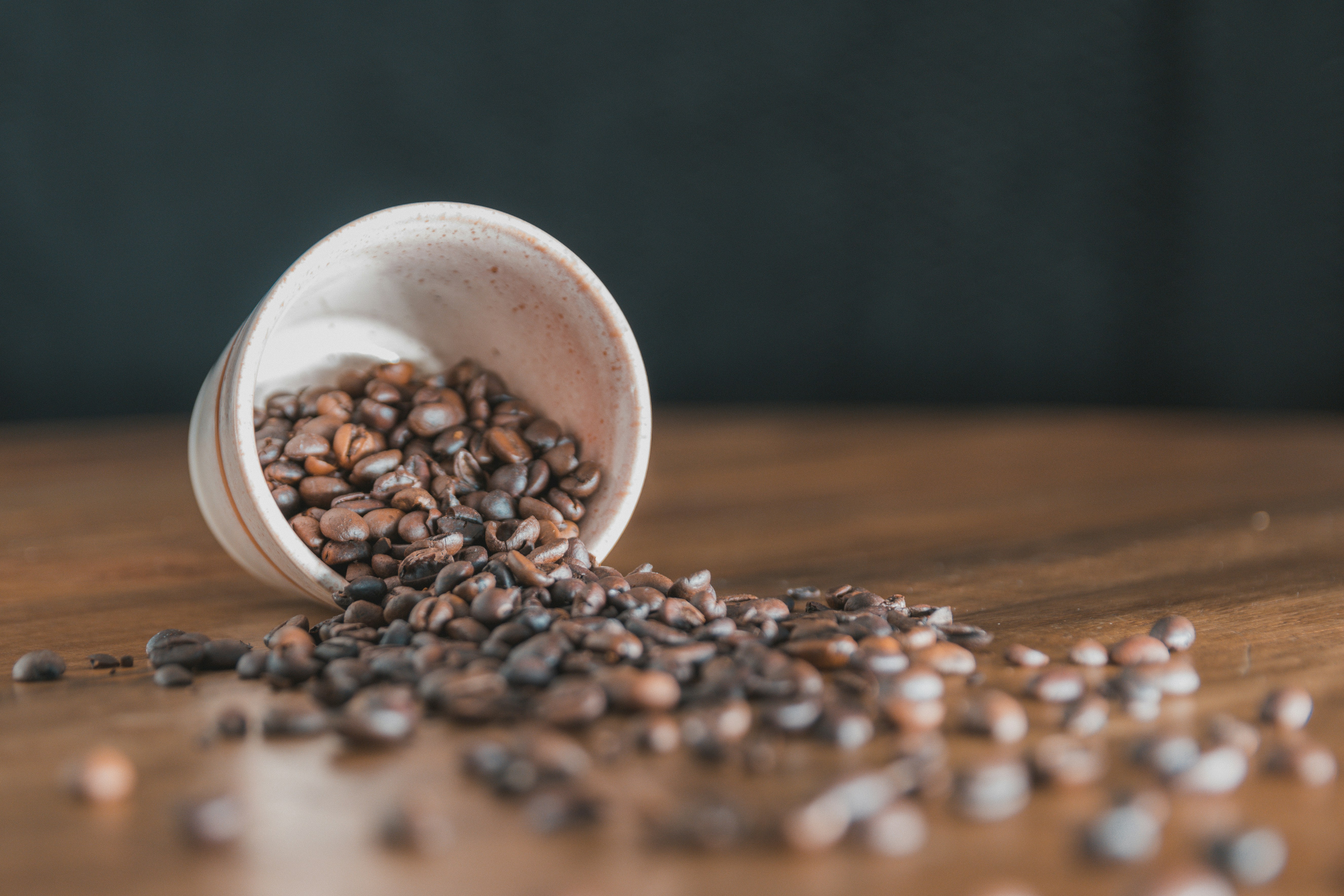 A picture of a cup of coffee beans spilled over a table.
