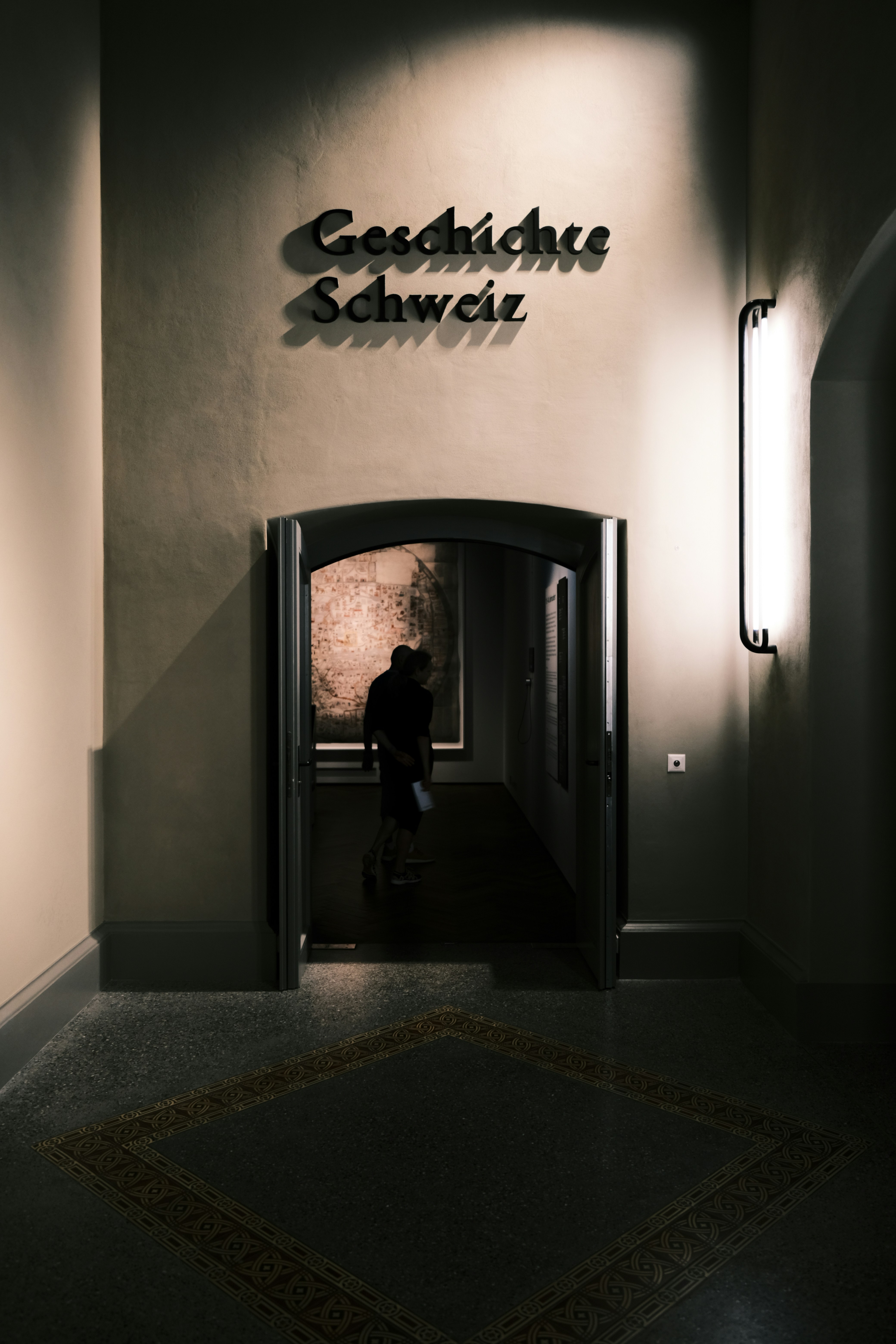 Doorway to Geschichte Schweiz: A Quiet Figure in a Dim Gallery