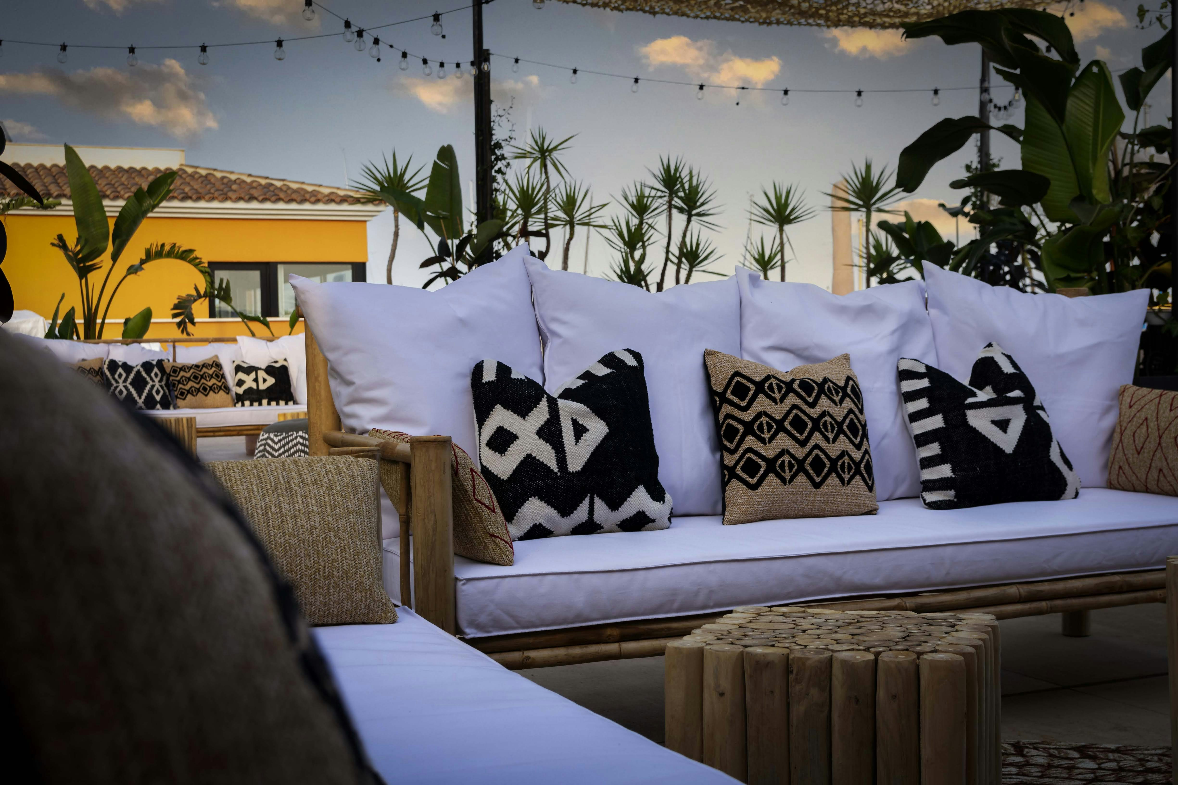 Stylish outdoor seating area featuring a wooden sofa adorned with patterned cushions, surrounded by lush greenery and ambient lighting.
