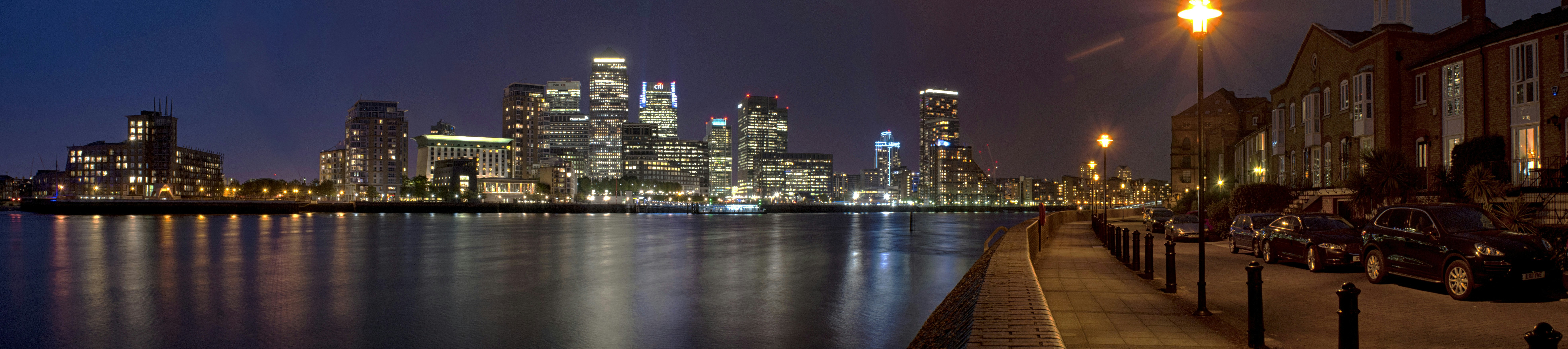 A panoramic view of a city skyline at night, illuminated by vibrant lights reflecting on the water's surface.
