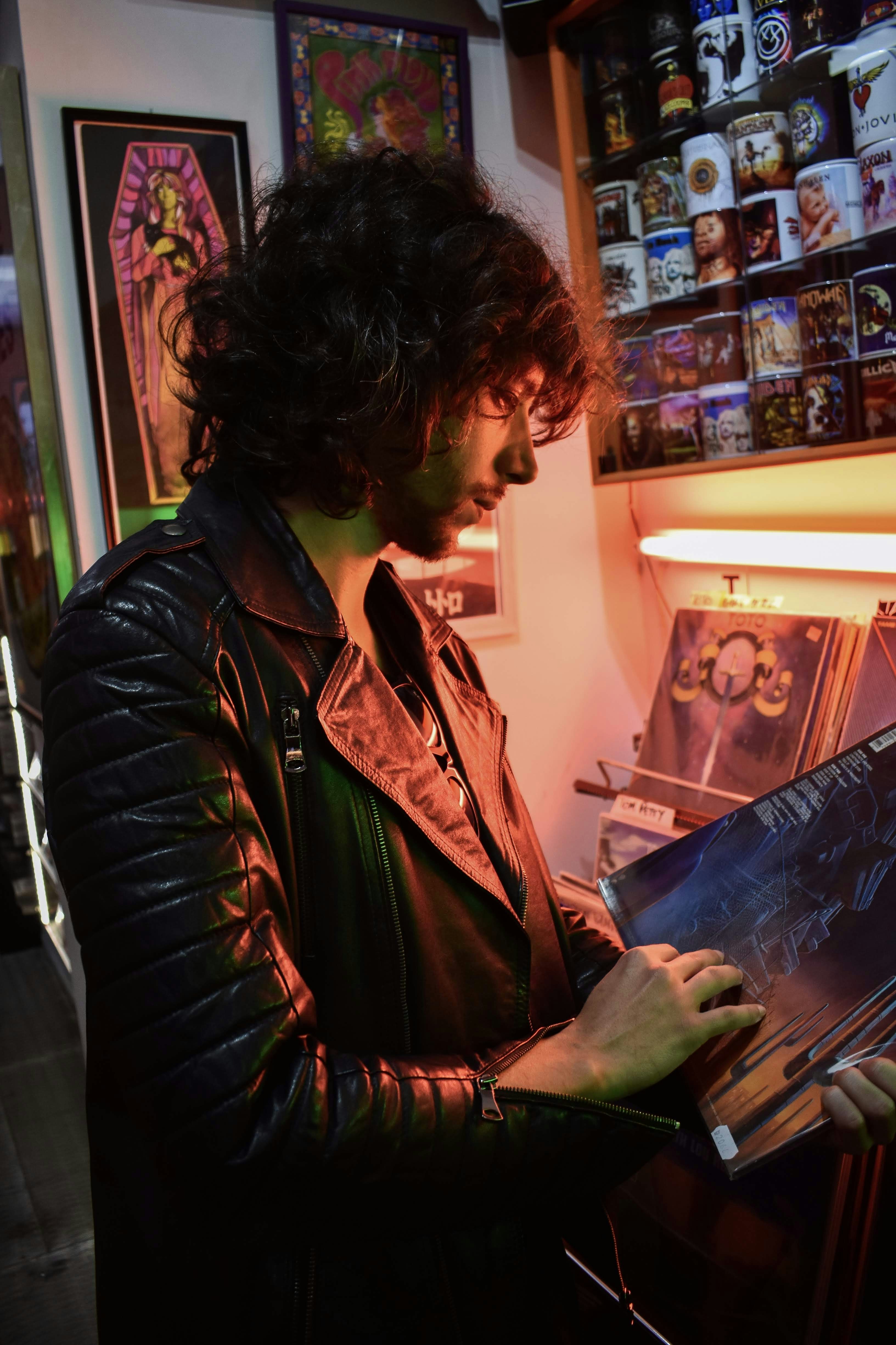 Person in a leather jacket browsing vinyl records in dimly lit shop.