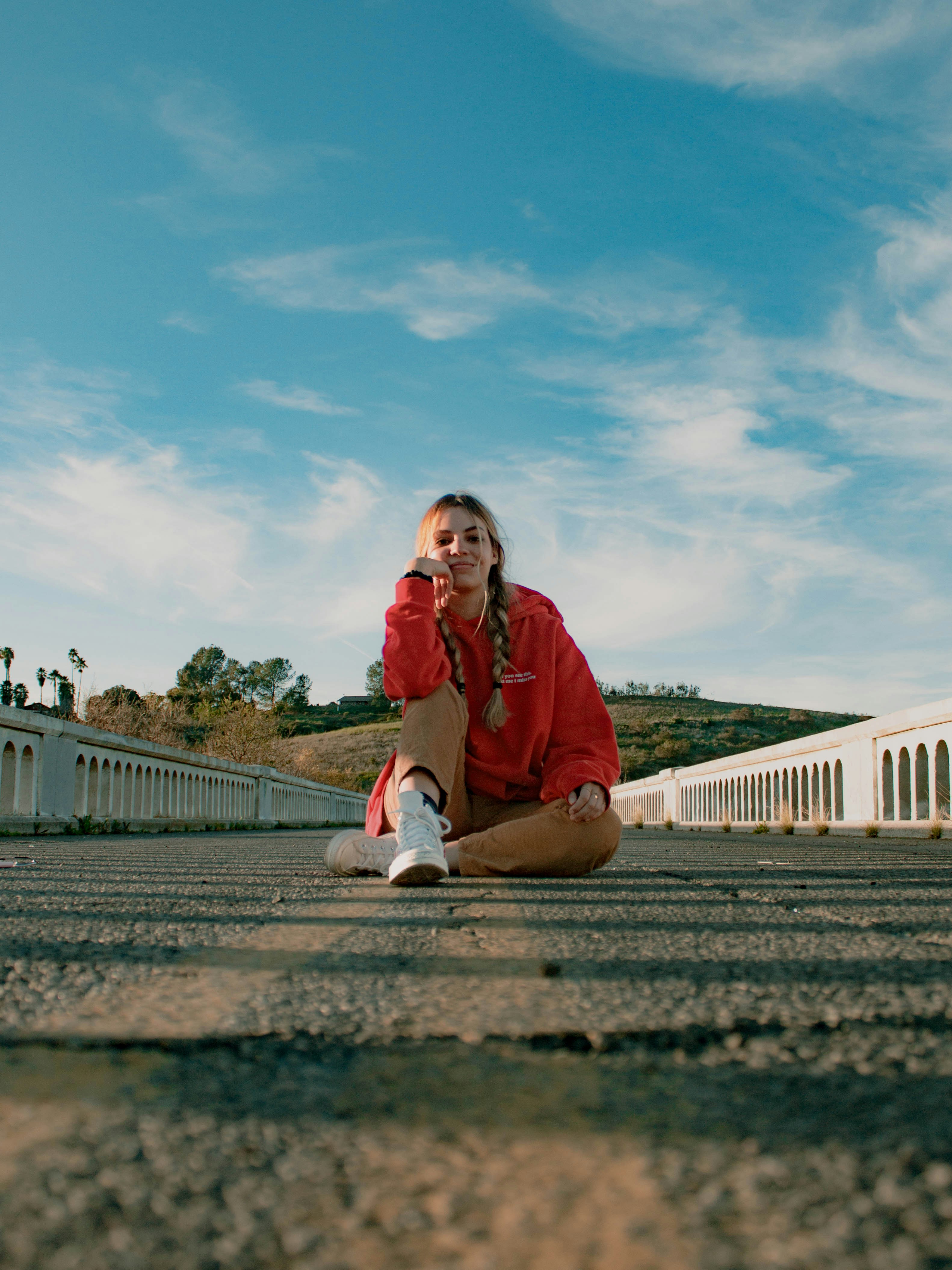 Person in a red jacket sitting thoughtfully on a bridge under a clear blue sky.