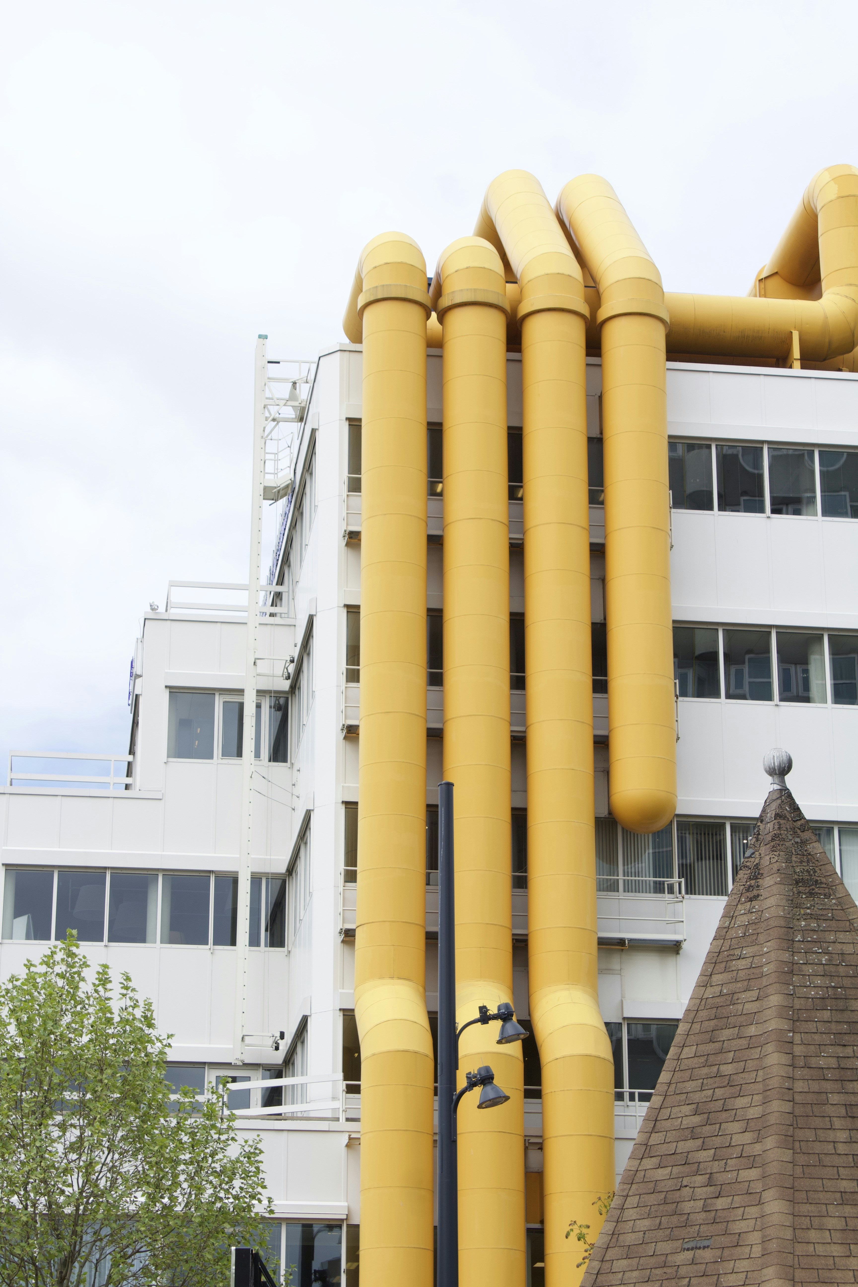 Vertical Golden Ducts Climb a White Industrial Facade