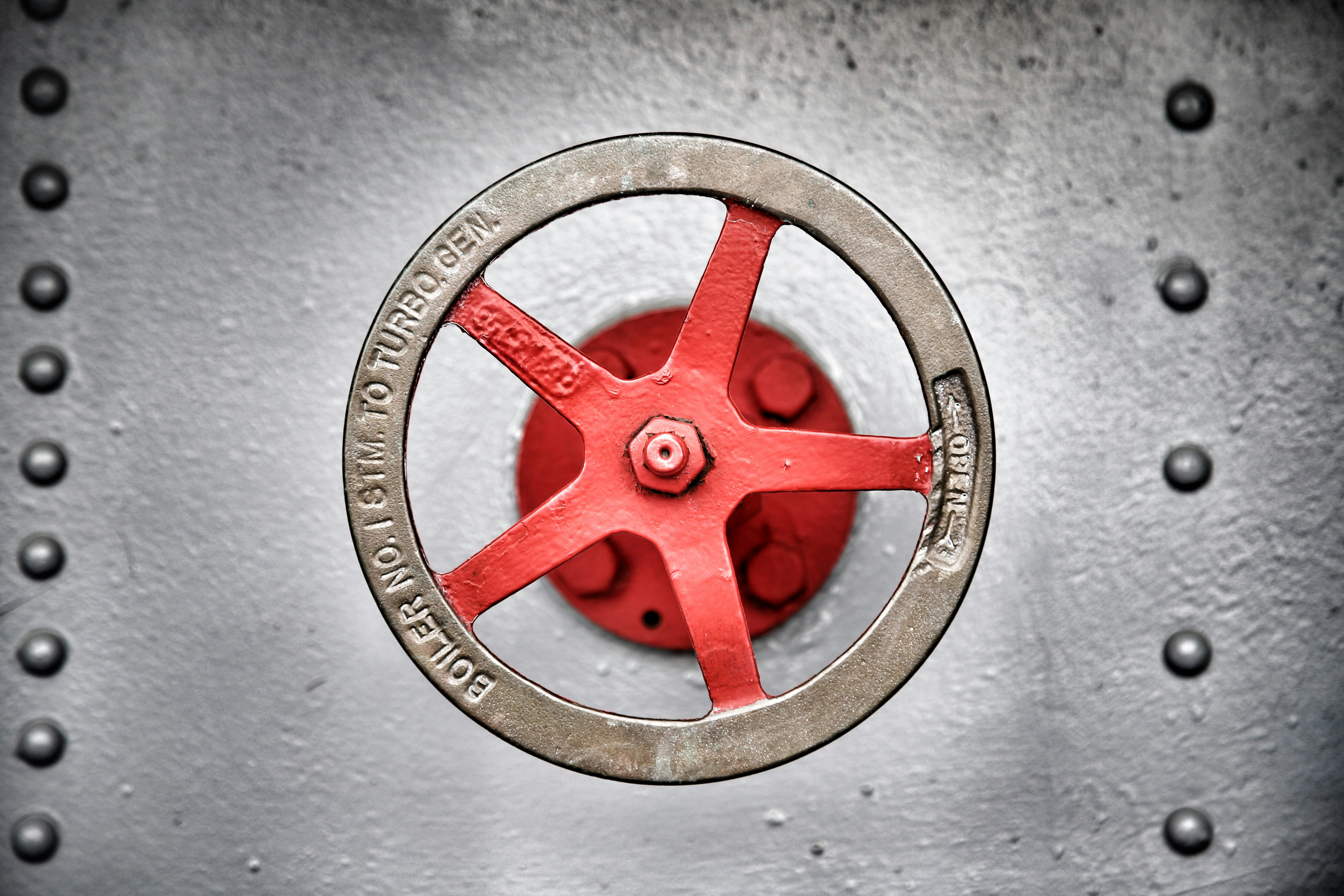 Red valve wheel framed by riveted metal plate