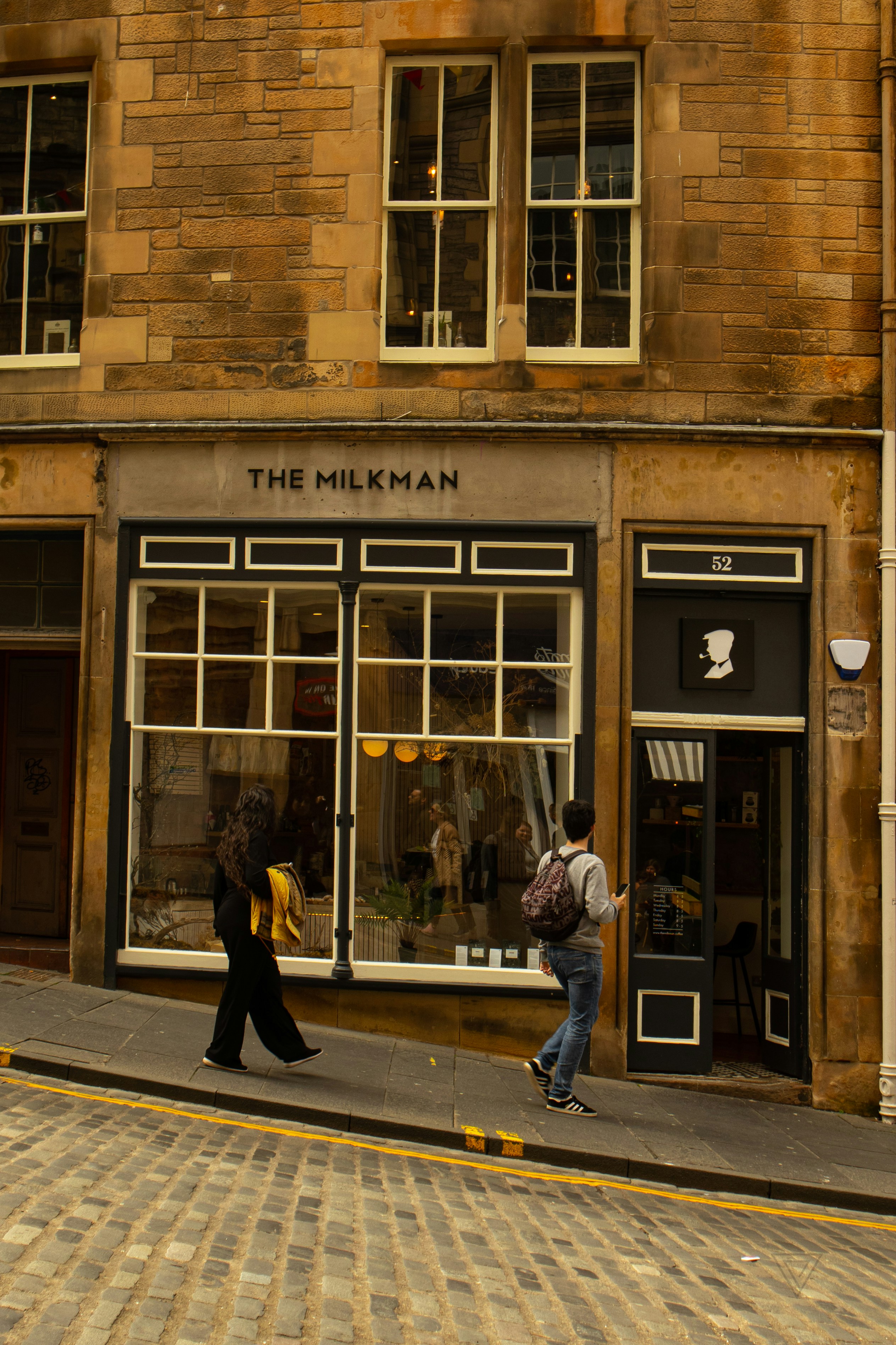 People walking past The Milkman café on a cobblestone street in Edinburgh.