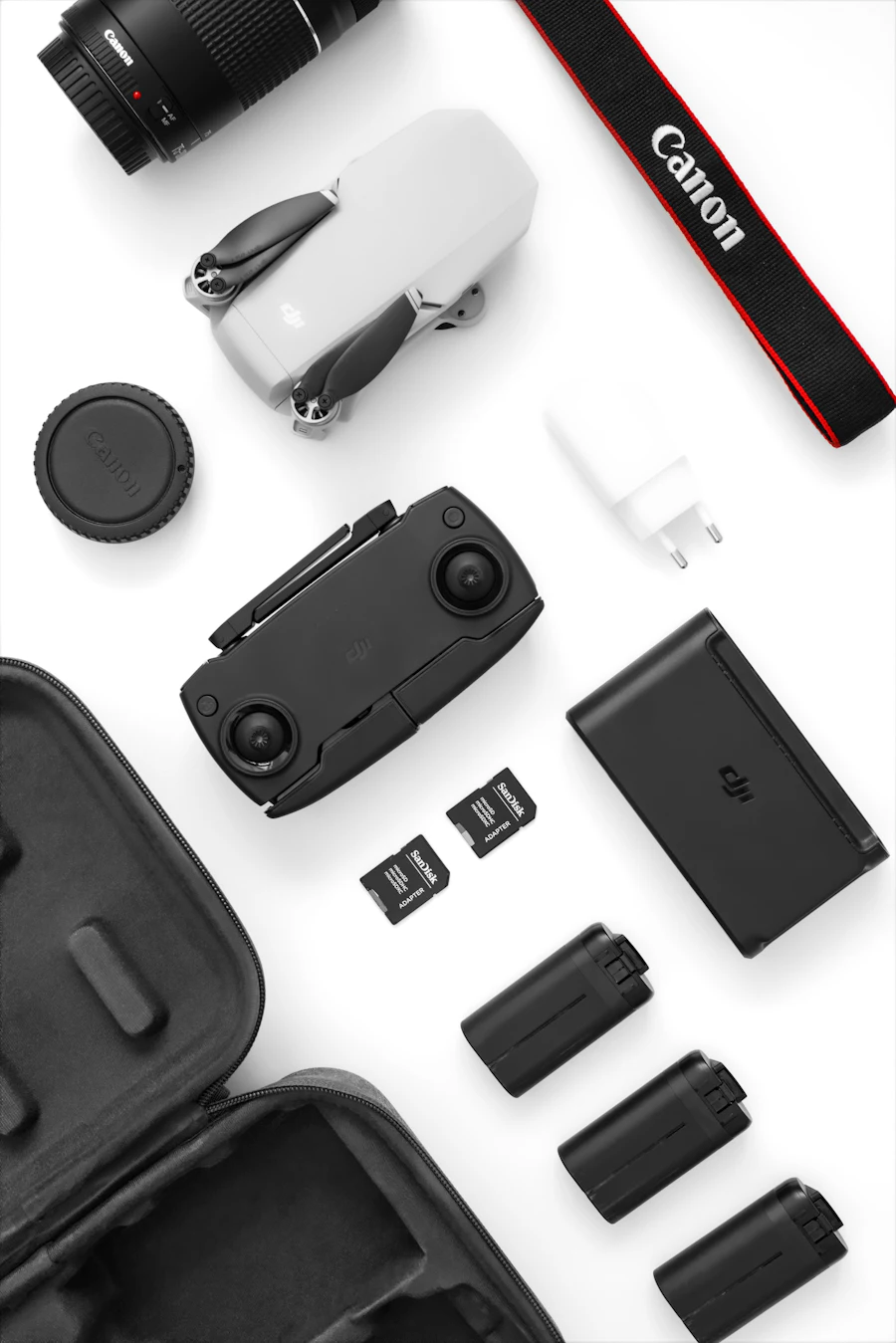 Flat lay of a folded DJI drone surrounded by Canon lens and strap, batteries, memory cards, charger, and carrying case on a white background.
