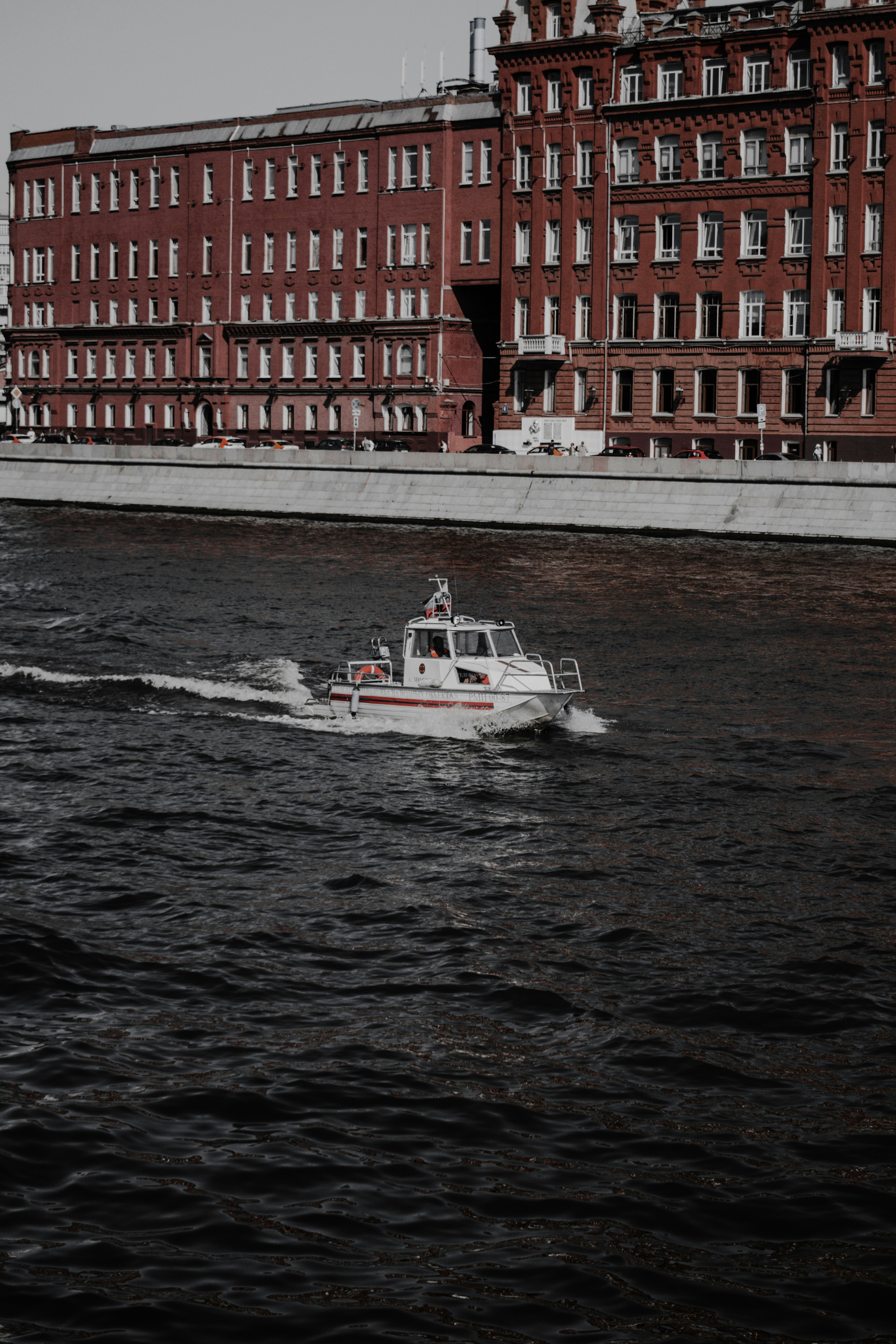 A Patrol Boat Carves a Wake Along a Brick-Red Riverside